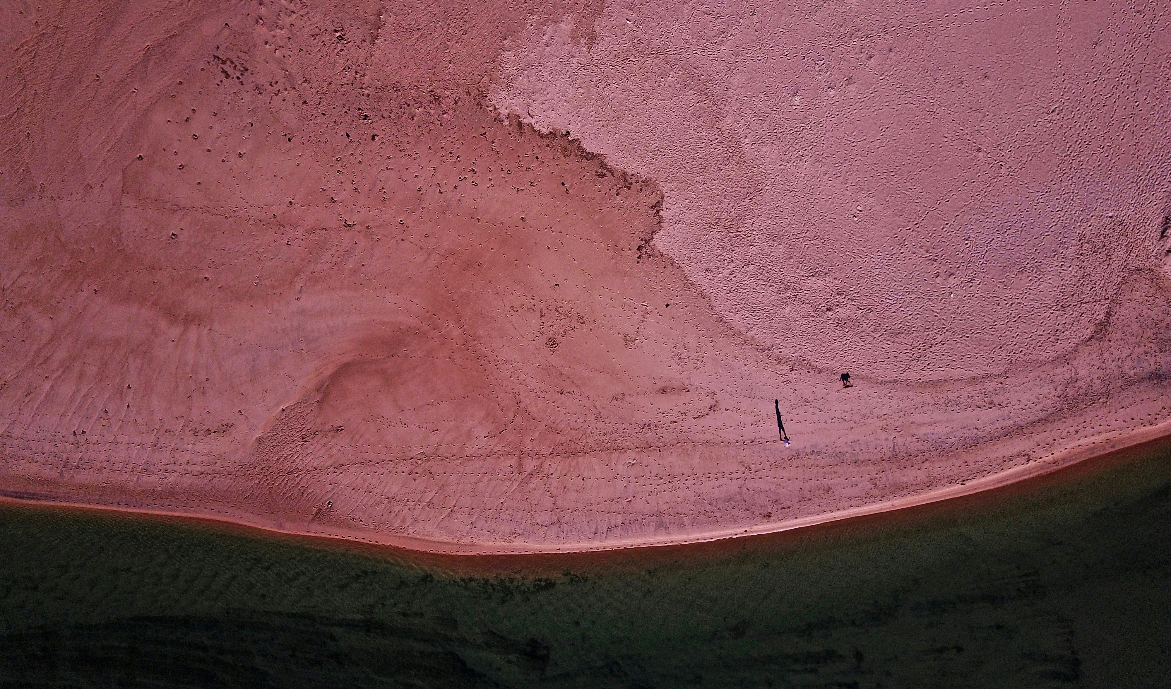 Aerial view showcasing a striking contrast between pink sandy terrain and a green water edge, highlighting the unique geological formations.
