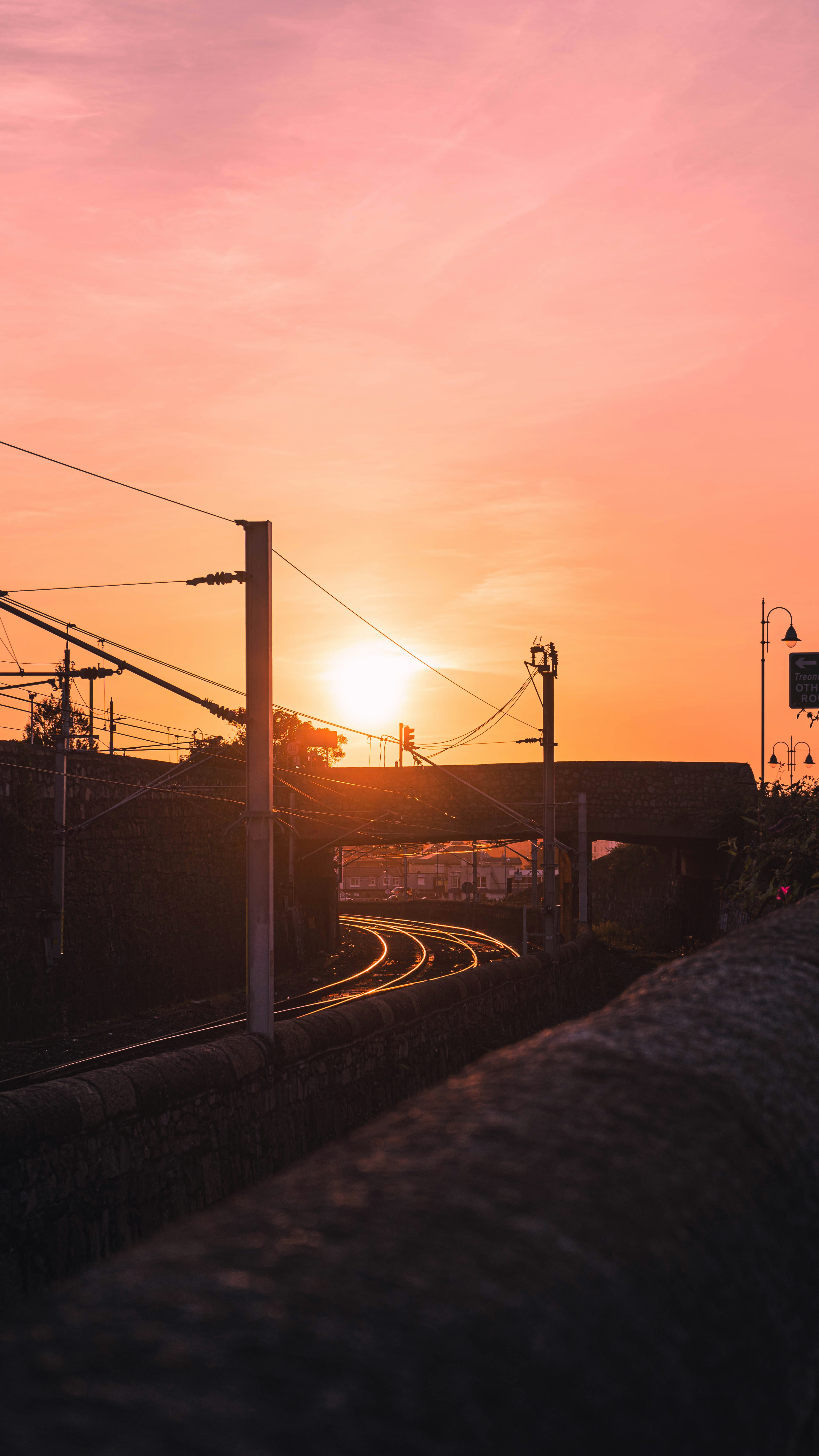 Sunset illuminating a railway scene, with tracks curving beneath a vibrant sky. The silhouette of infrastructure adds depth to the tranquil moment.