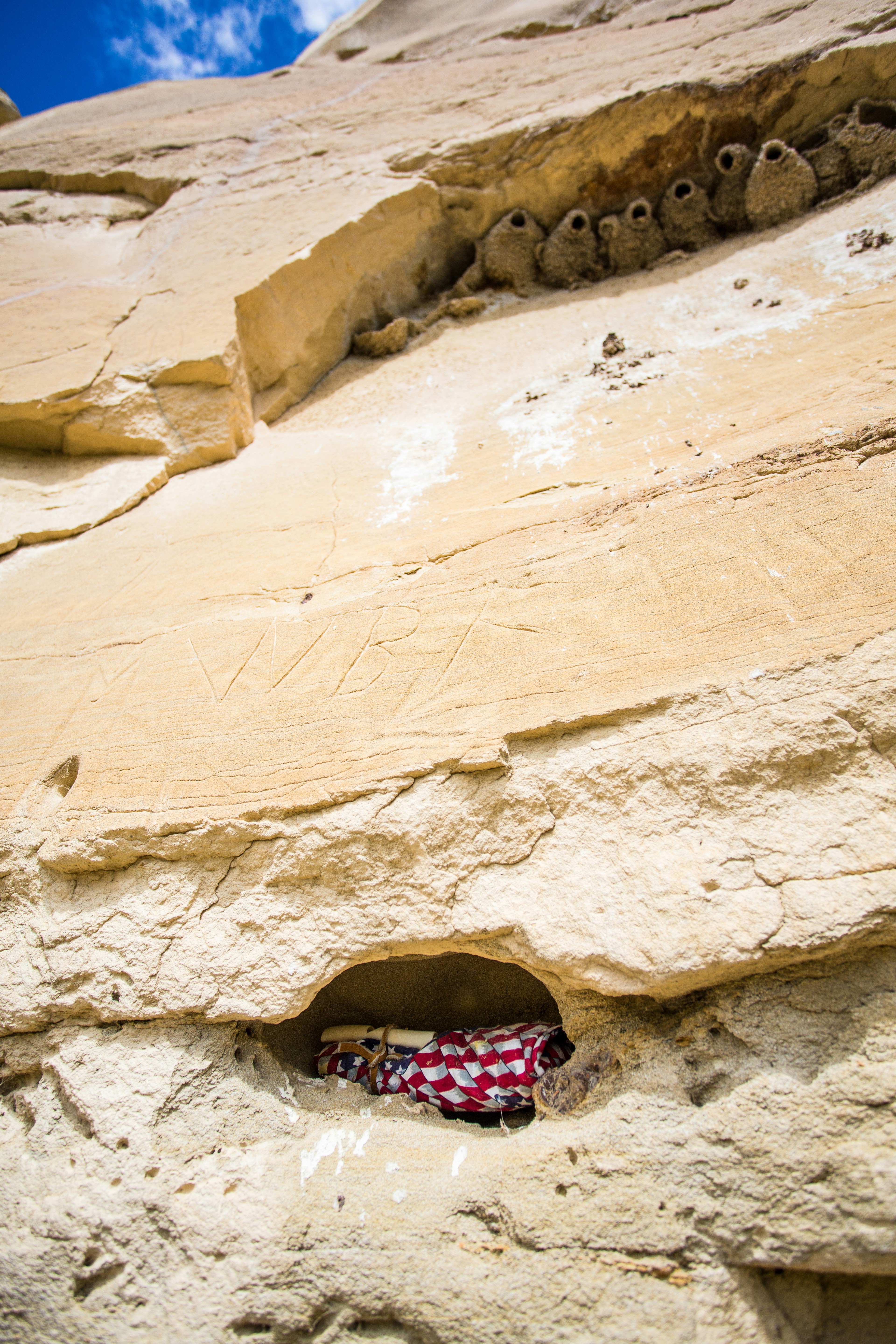 Prayer flags and a pipe nestled in a sandstone crevice at Deer Medicine Rocks under a clear blue sky.