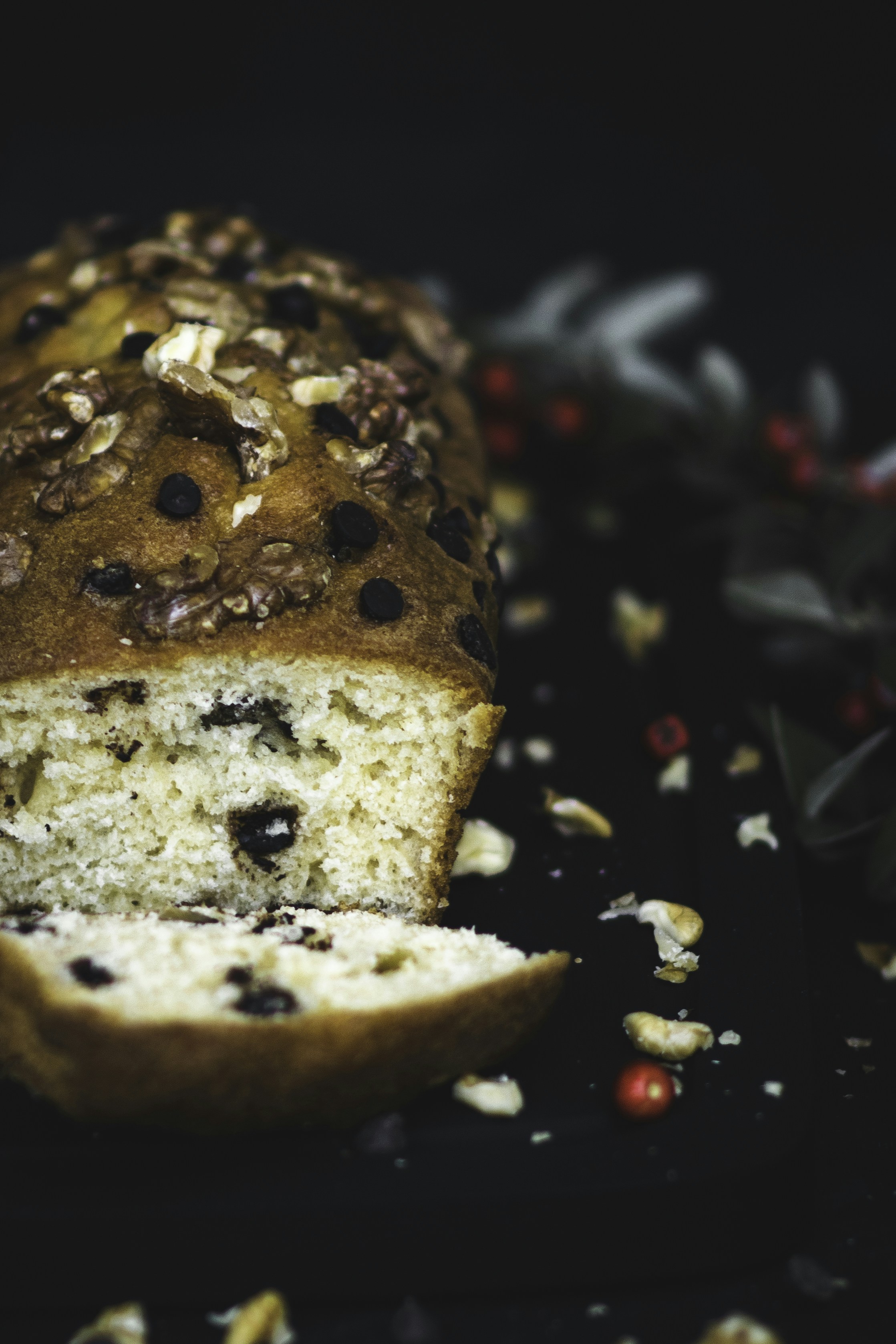 Freshly baked loaf adorned with nuts and chocolate chips, resting on a dark surface with scattered crumbs.
