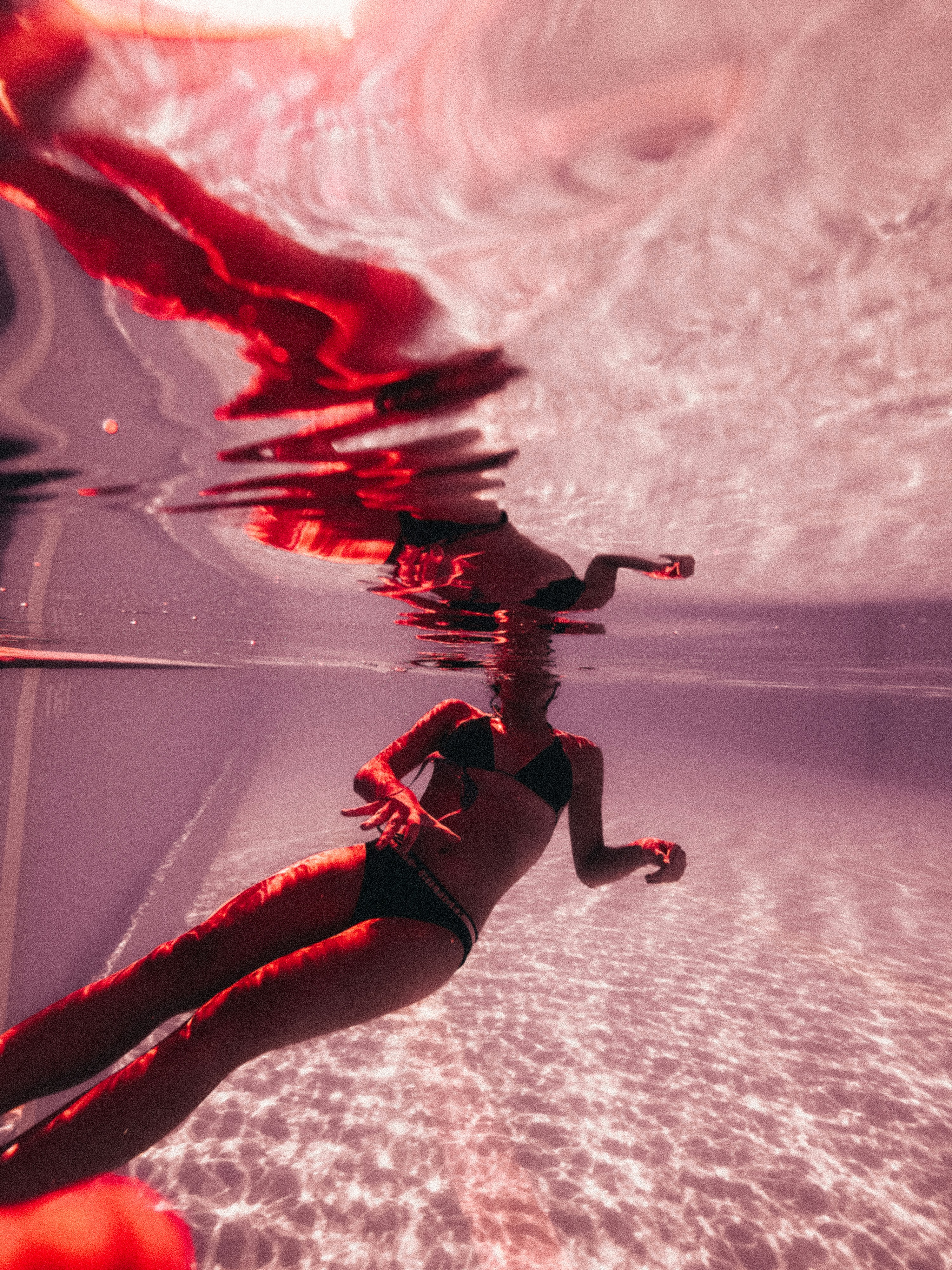 Underwater photograph of a swimmer gliding just beneath the surface, pink-tinted light rippling across the water.