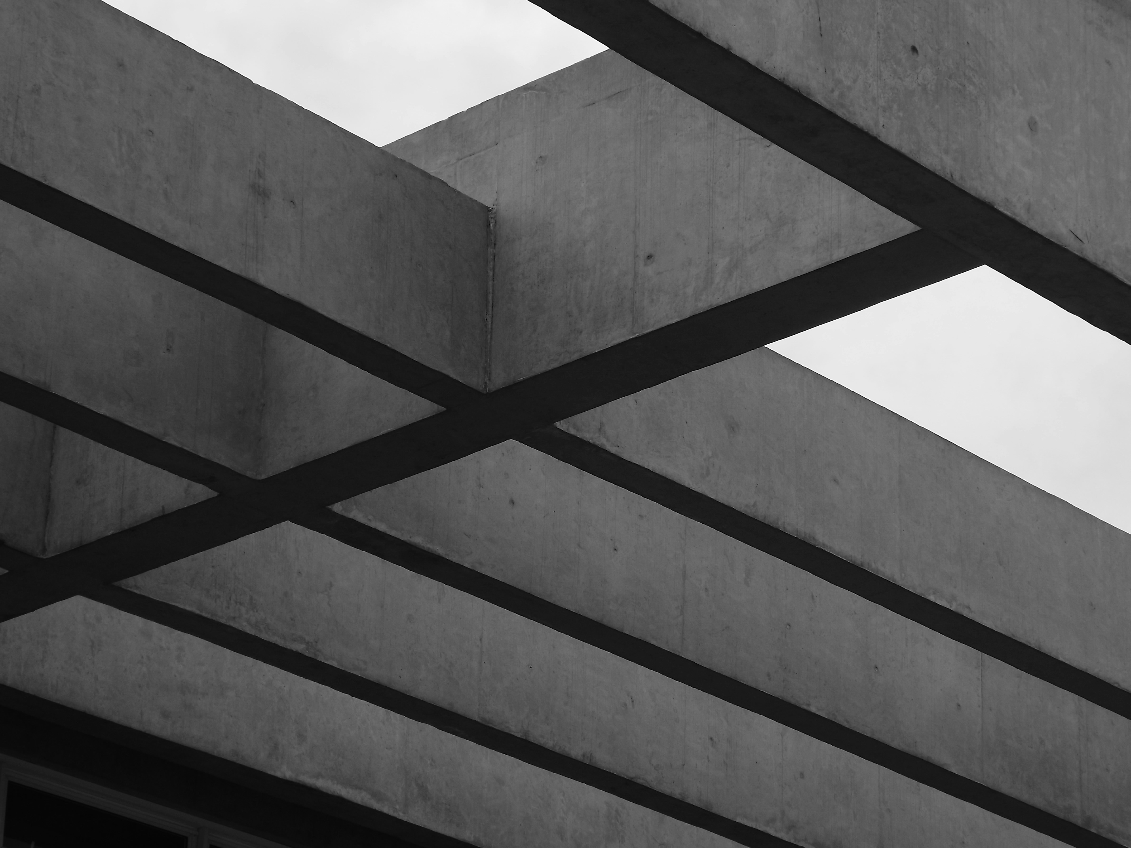 Grayscale architectural beams form a geometric pattern against a cloudy sky.