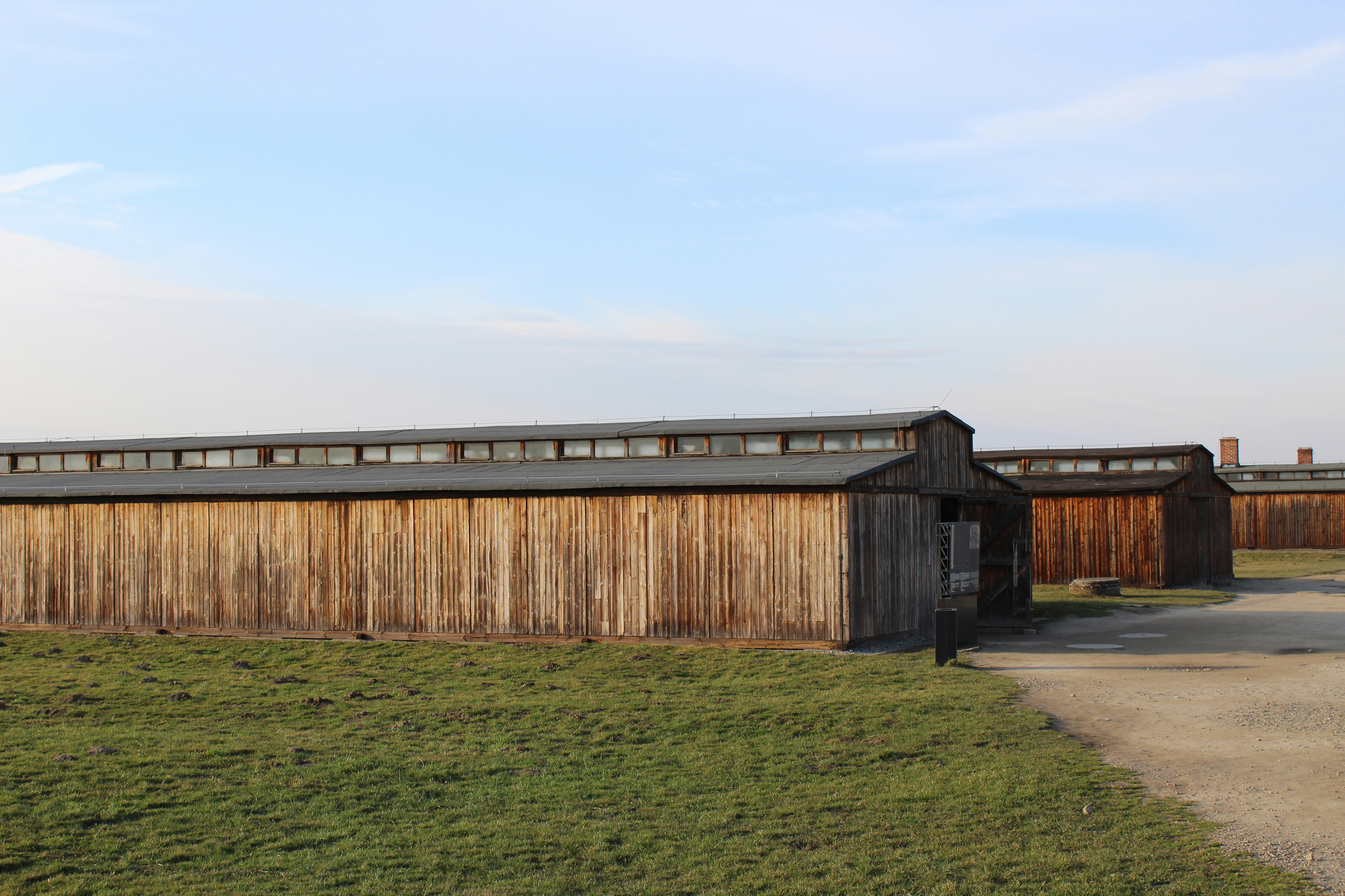 Long wooden building with a dark roof set against a bright blue sky and grassy foreground.