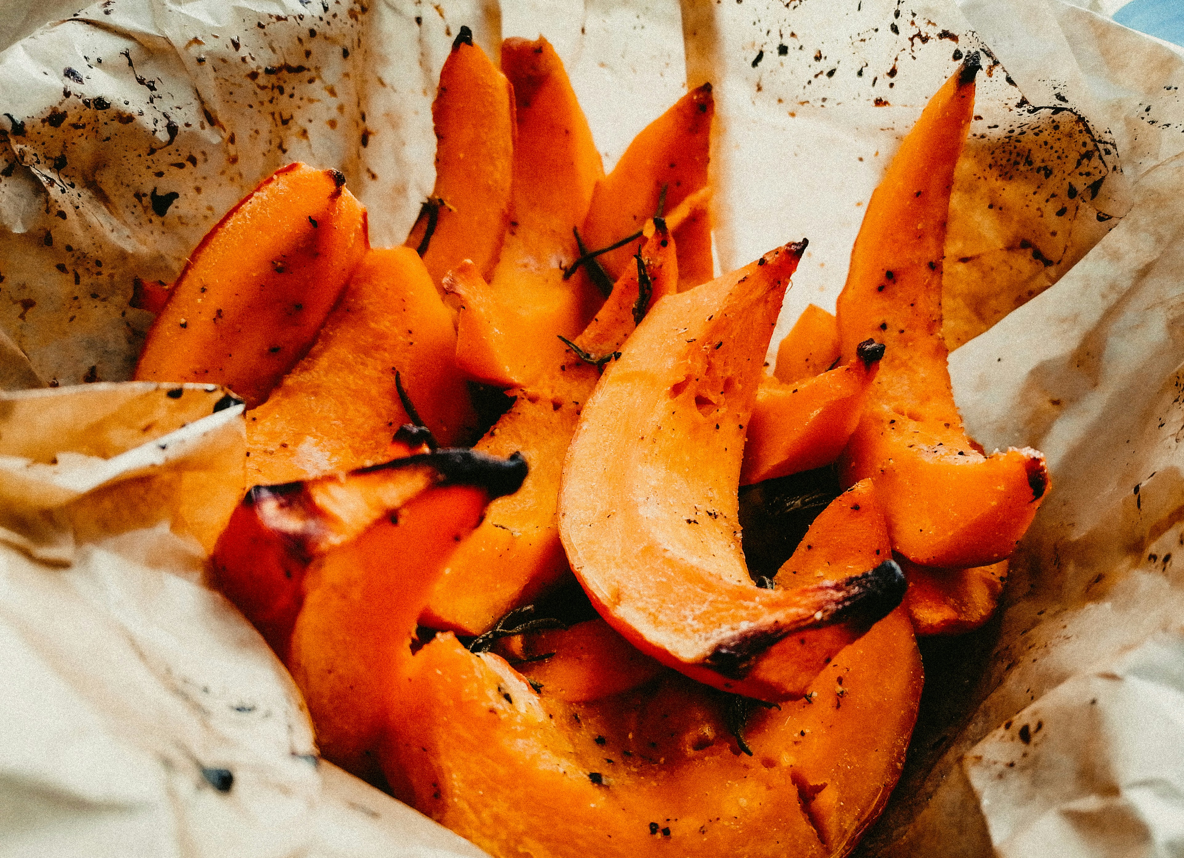 Slices of roasted pumpkin nestled in parchment paper, showcasing vibrant orange tones and rustic textures.