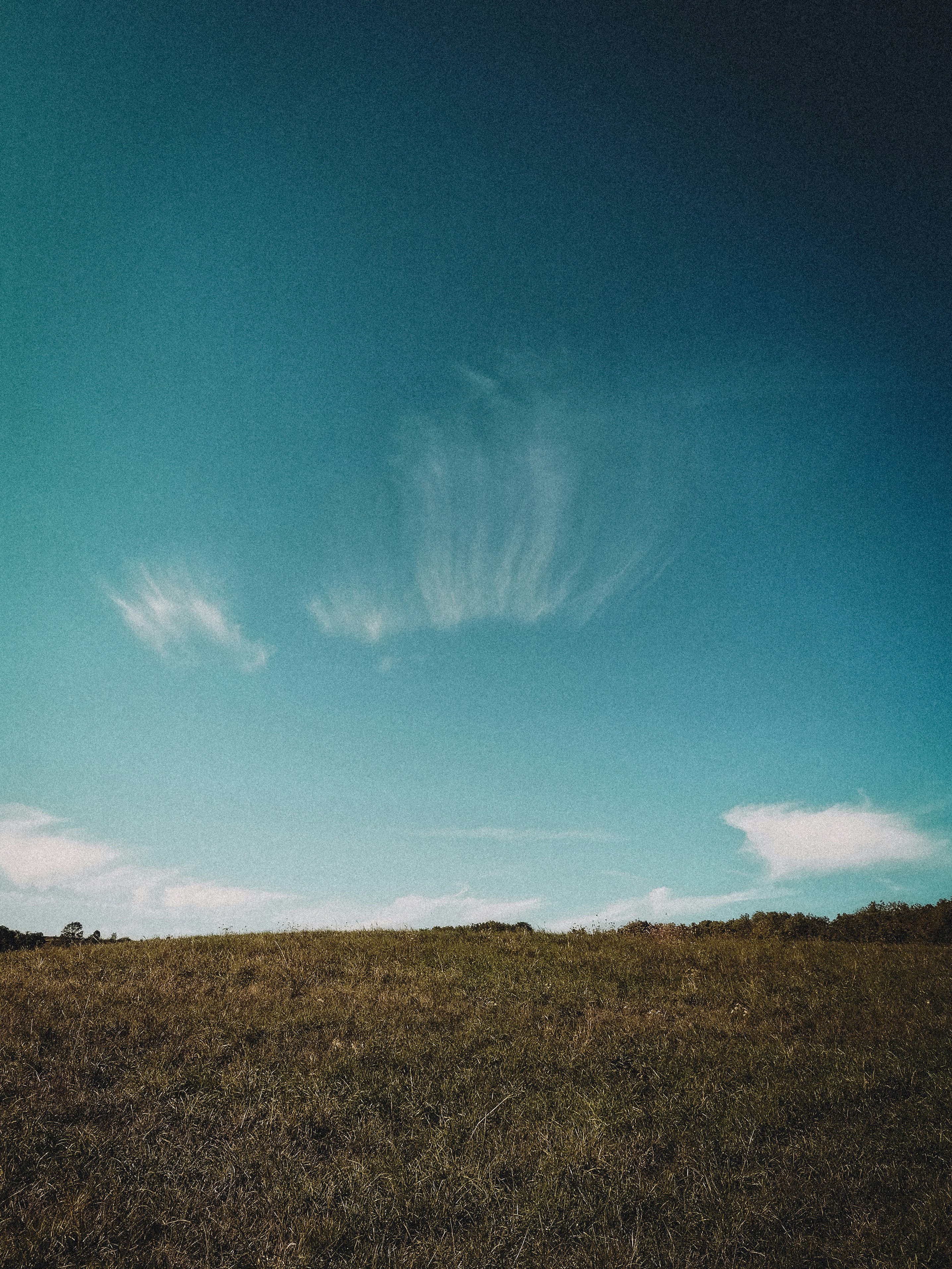 Vast expanse of blue sky adorned with wispy clouds above a gentle grassy hill. The scene evokes a sense of serenity and openness.