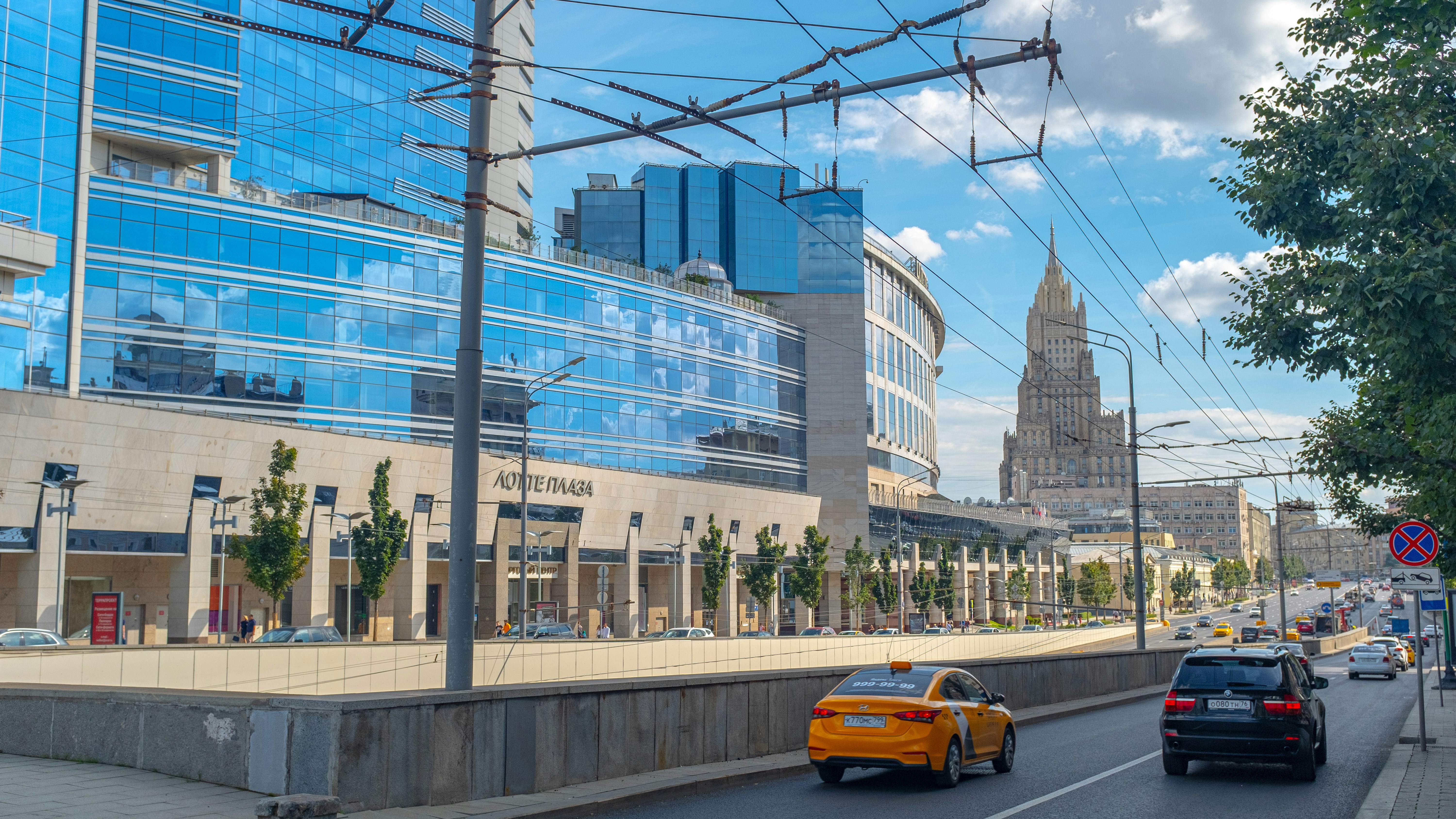Sunlit Glass Corridor: An Orange Taxi Meanders Past Modern Facades