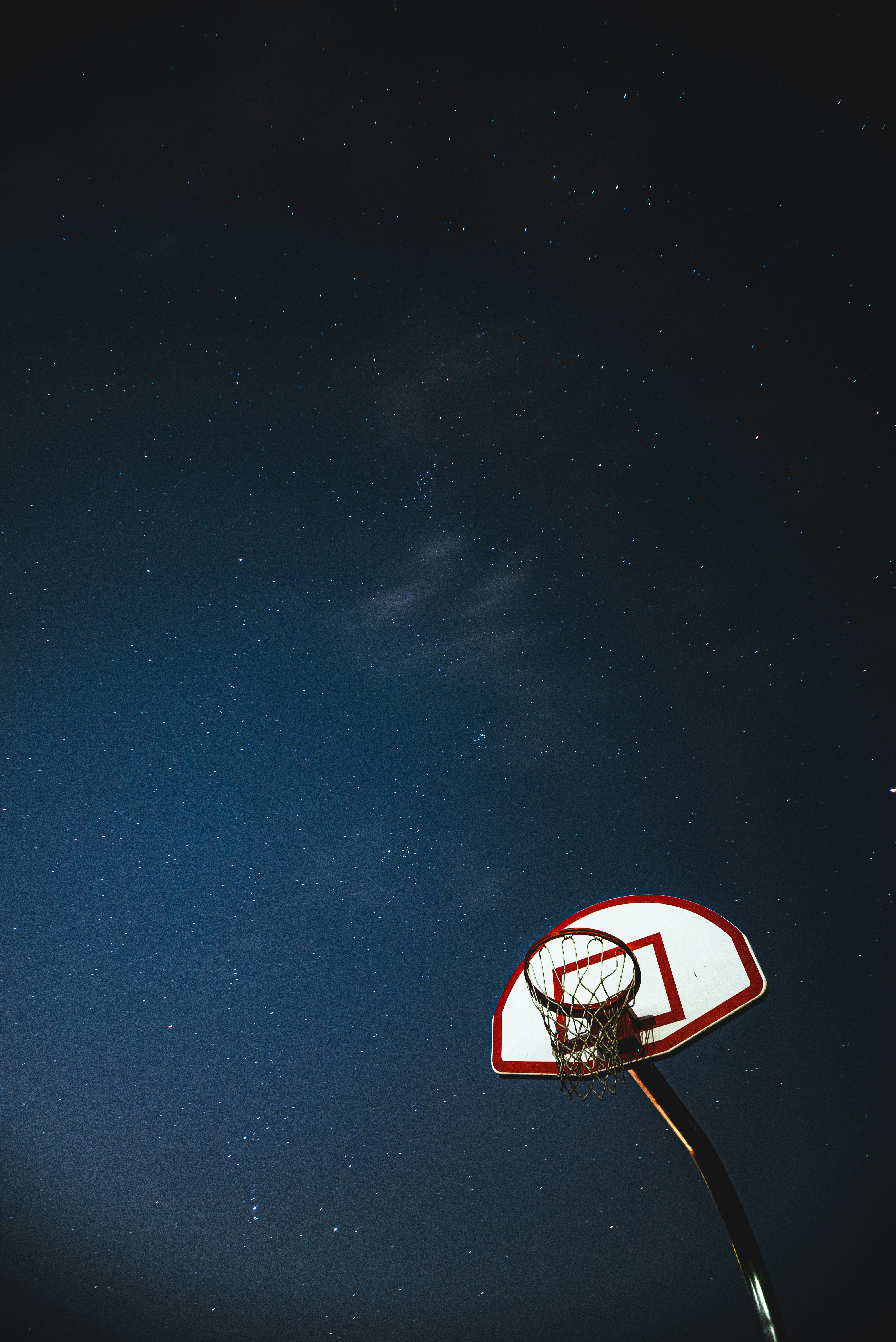 Basketball hoop silhouetted against a starry night sky, capturing the essence of play under the cosmos.