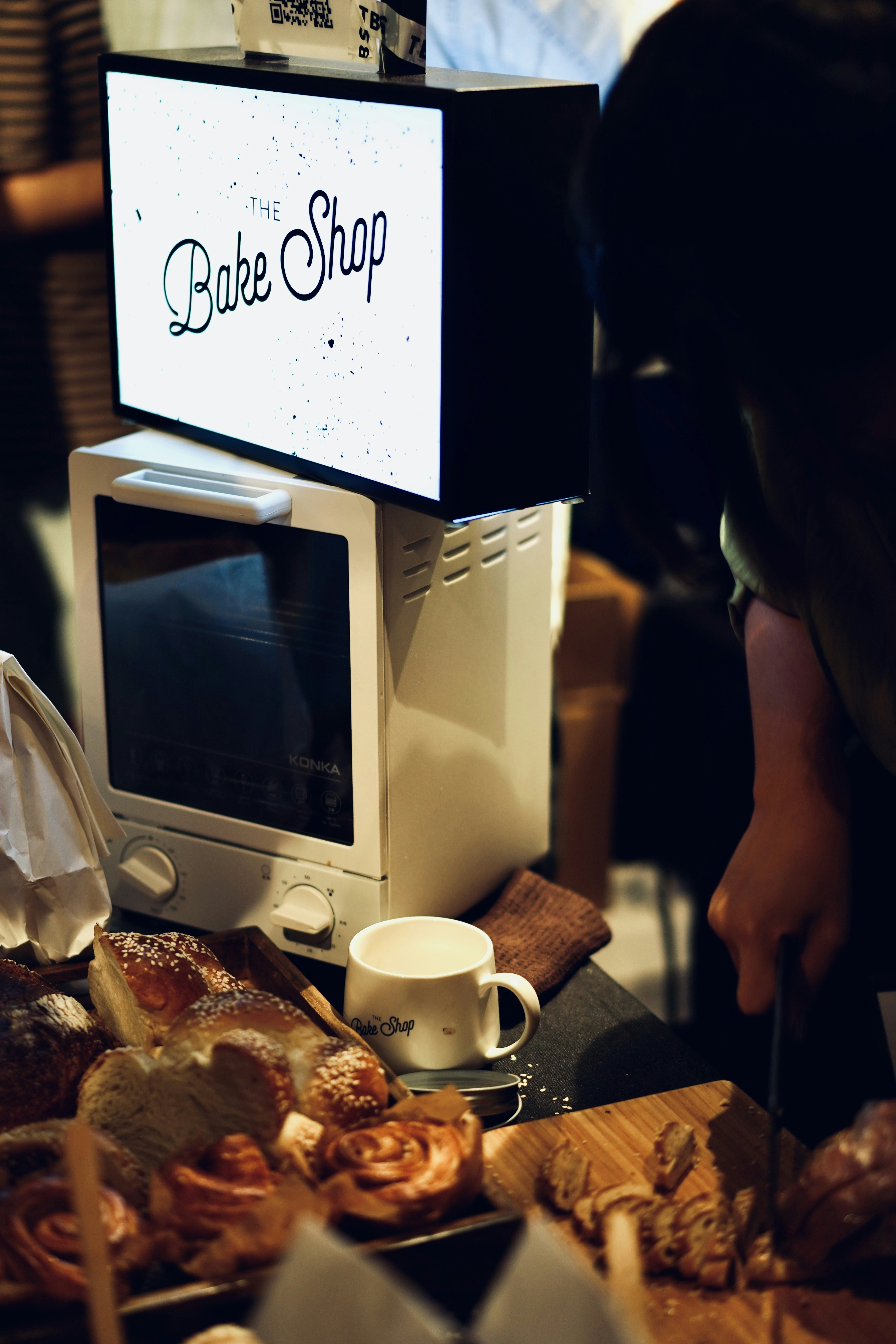 Bakery counter with a monitor displaying a stylized 'The Babe Shop' logo above a tray of croissants and pastries.