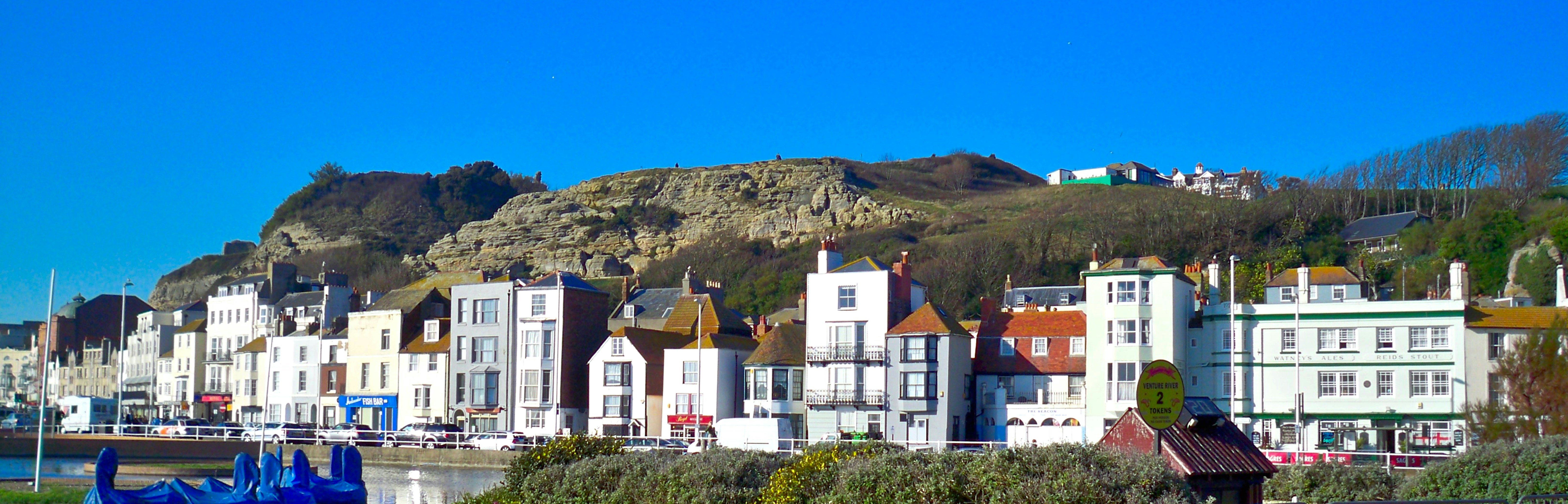 Historic seaside buildings with colorful facades set against a backdrop of rugged cliffs under a clear blue sky.