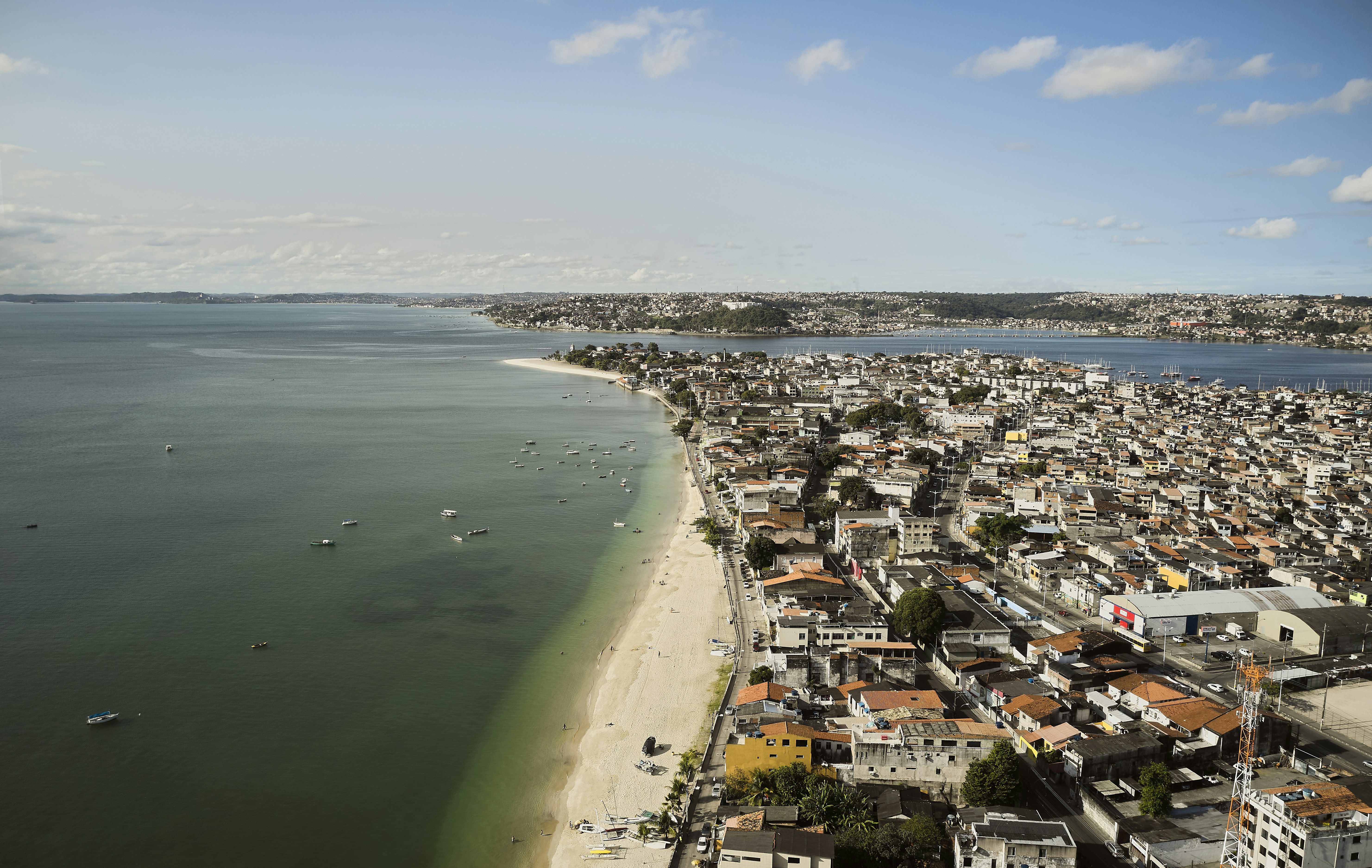 Aerial view of a coastal cityscape with a sandy beach meeting the tranquil ocean under a clear blue sky.