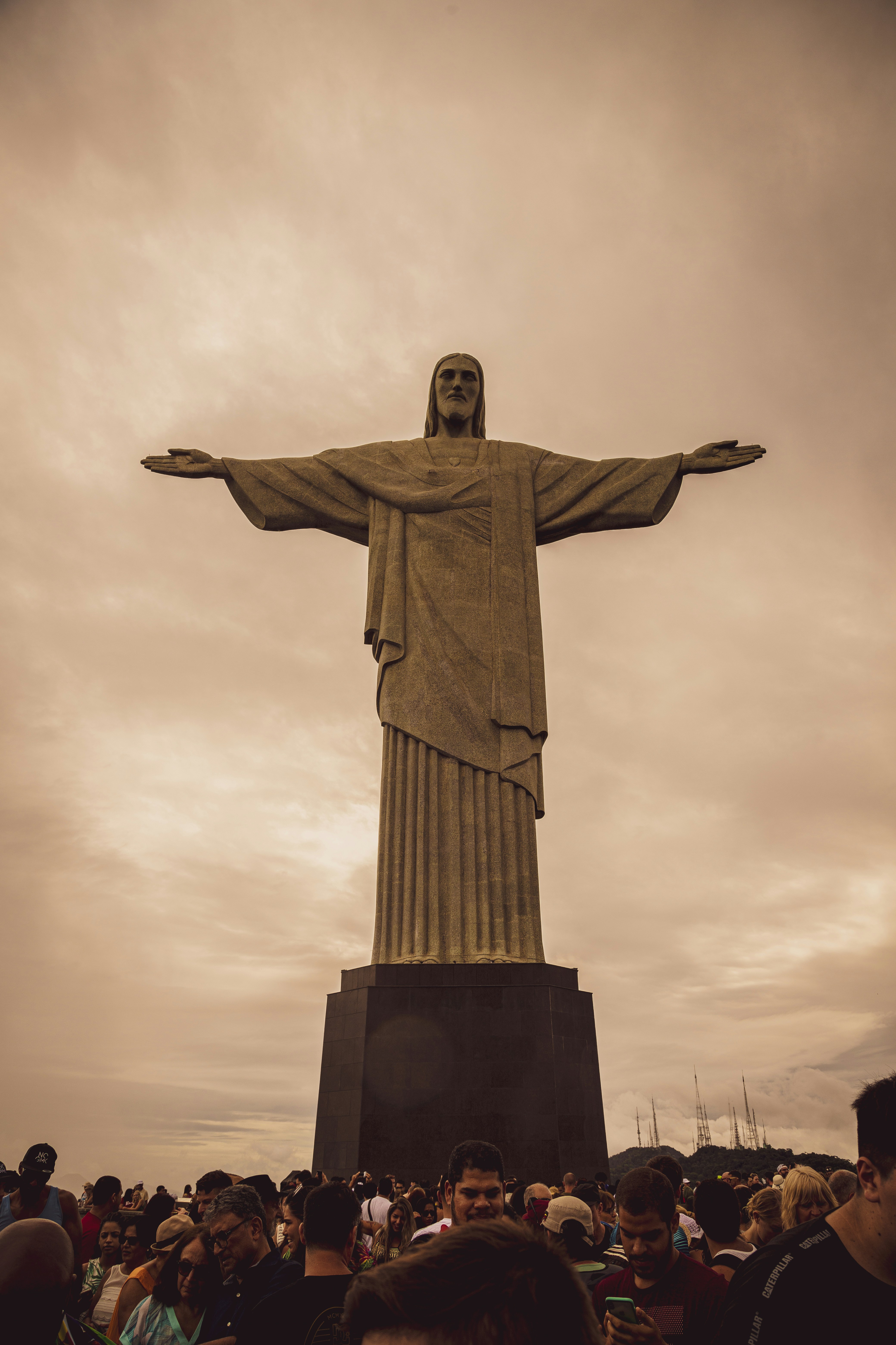 Christ the Redeemer statue towers over a crowd of visitors, symbolizing peace and unity against a cloudy sky.