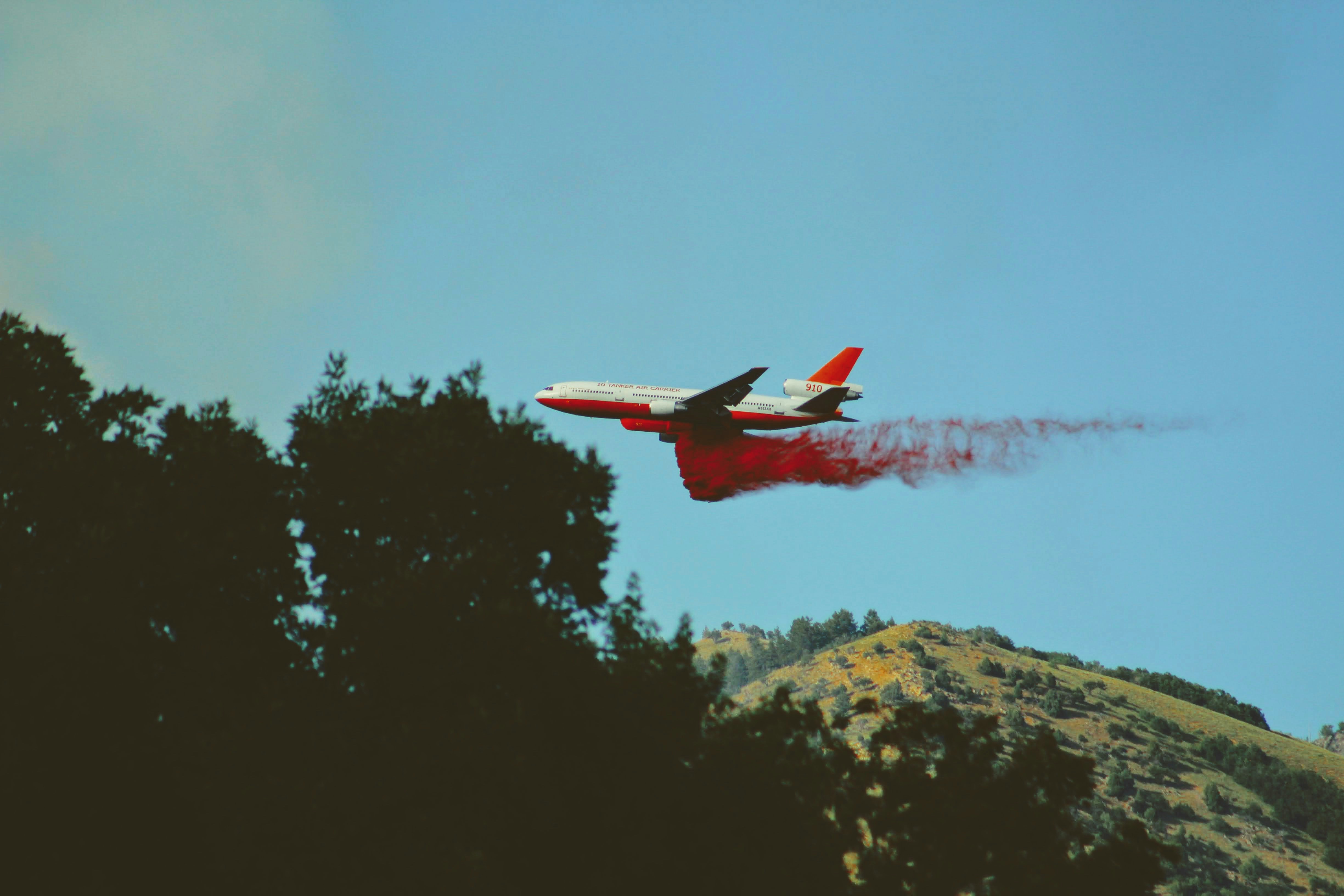 Airplane releasing fire retardant over a mountainous landscape, surrounded by trees.