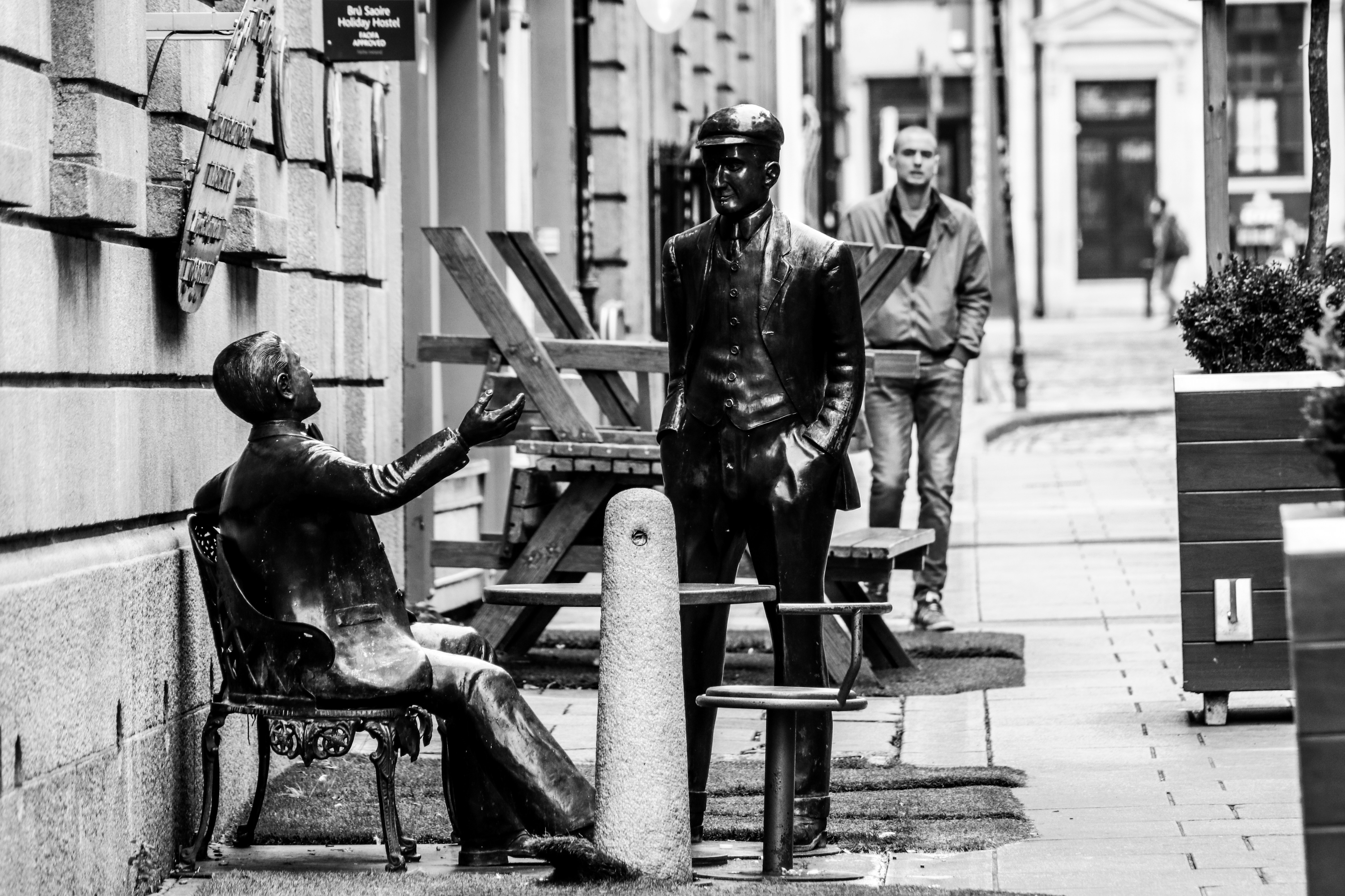 Bronze statues of two men engaged in conversation on a city street, with a passerby in the background. The scene captures a blend of art and urban life.