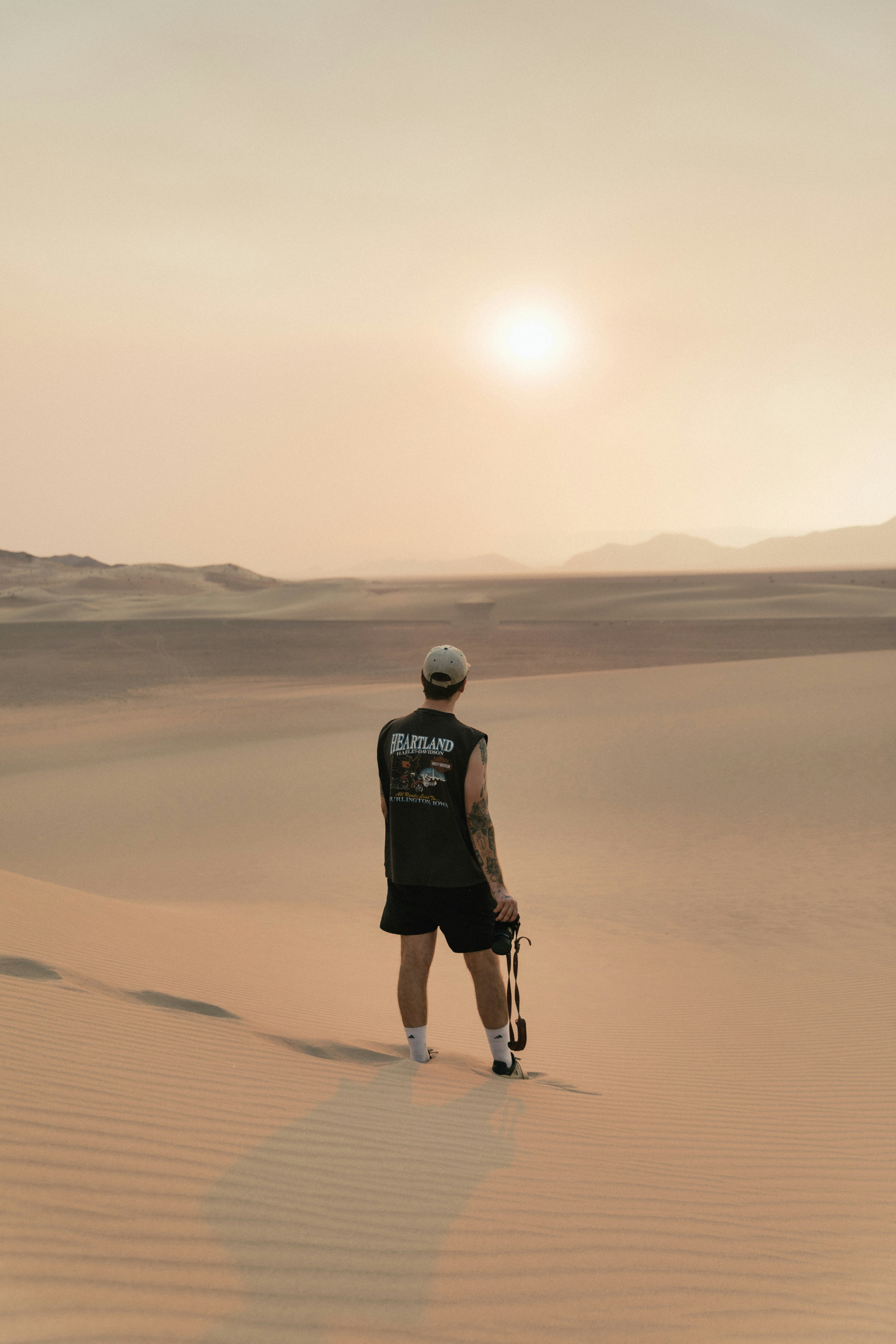 Desert Portrait at Dusk: A lone figure stands in wind-sculpted dunes as the sun fades