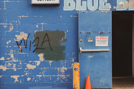 Orange Cone Guards a Cracked Blue Wall and Open Door