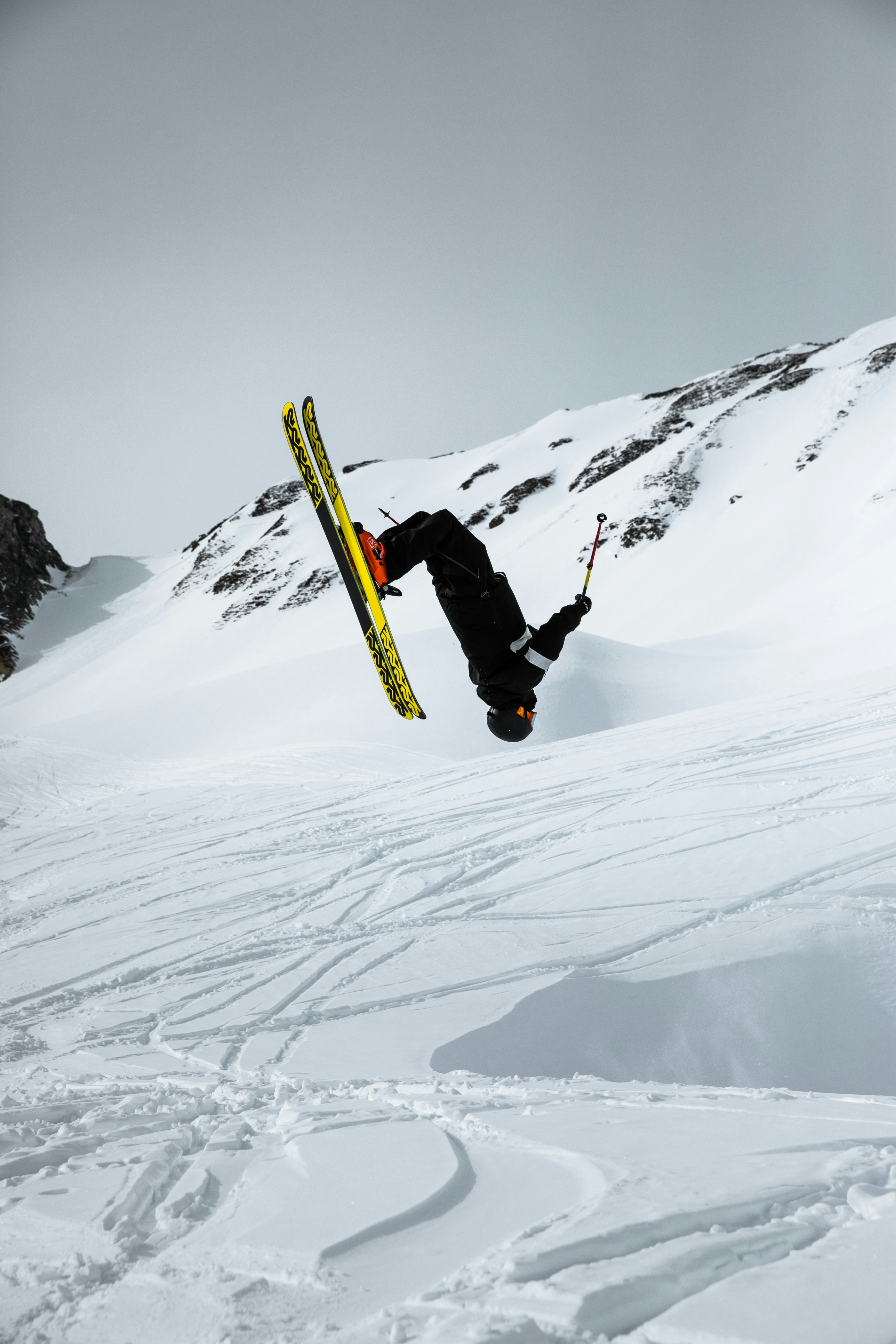 Skier performing a backflip over a snow-covered slope, showcasing athleticism against a dramatic mountainous backdrop.