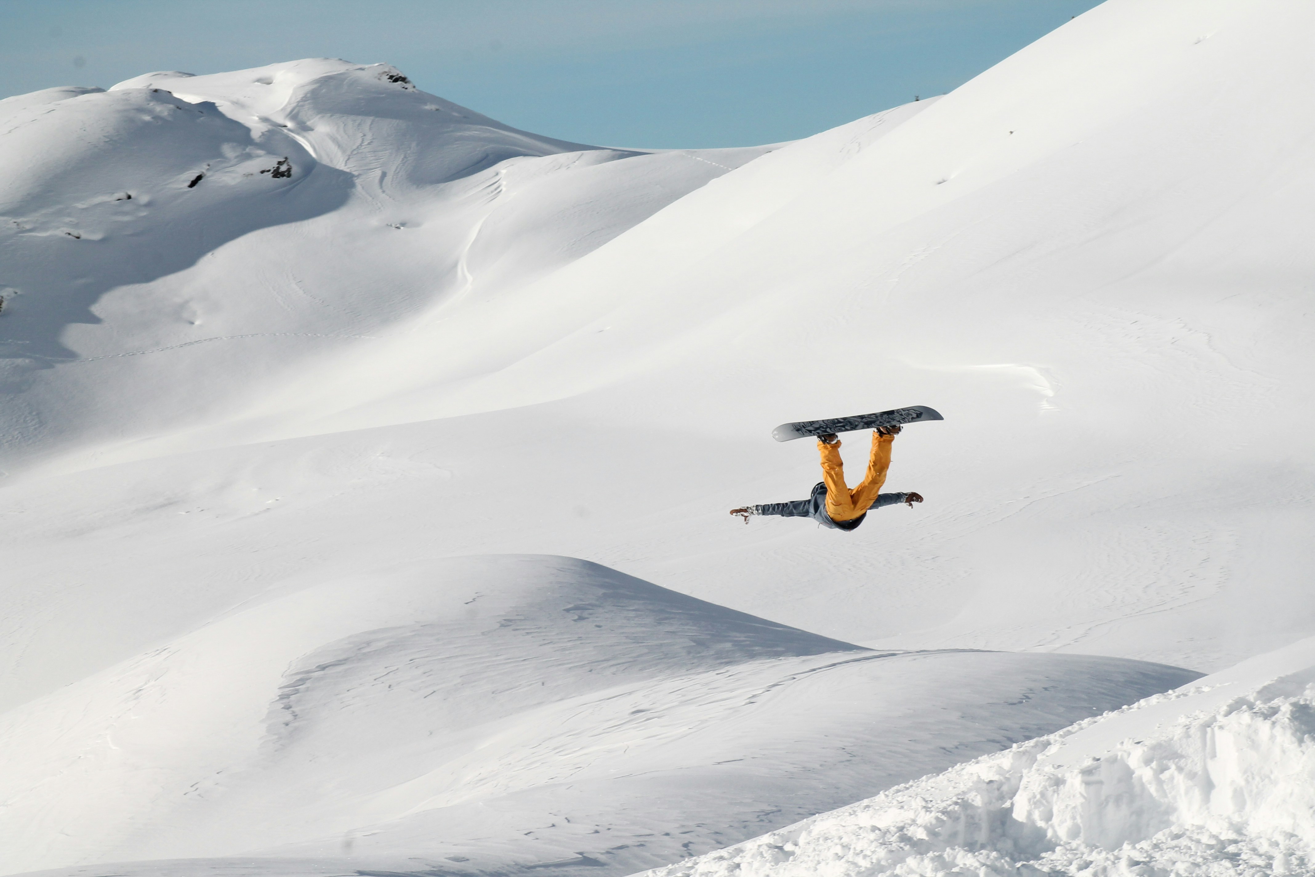 A snowboarder performs an impressive aerial maneuver against a backdrop of pristine snow-covered mountains.