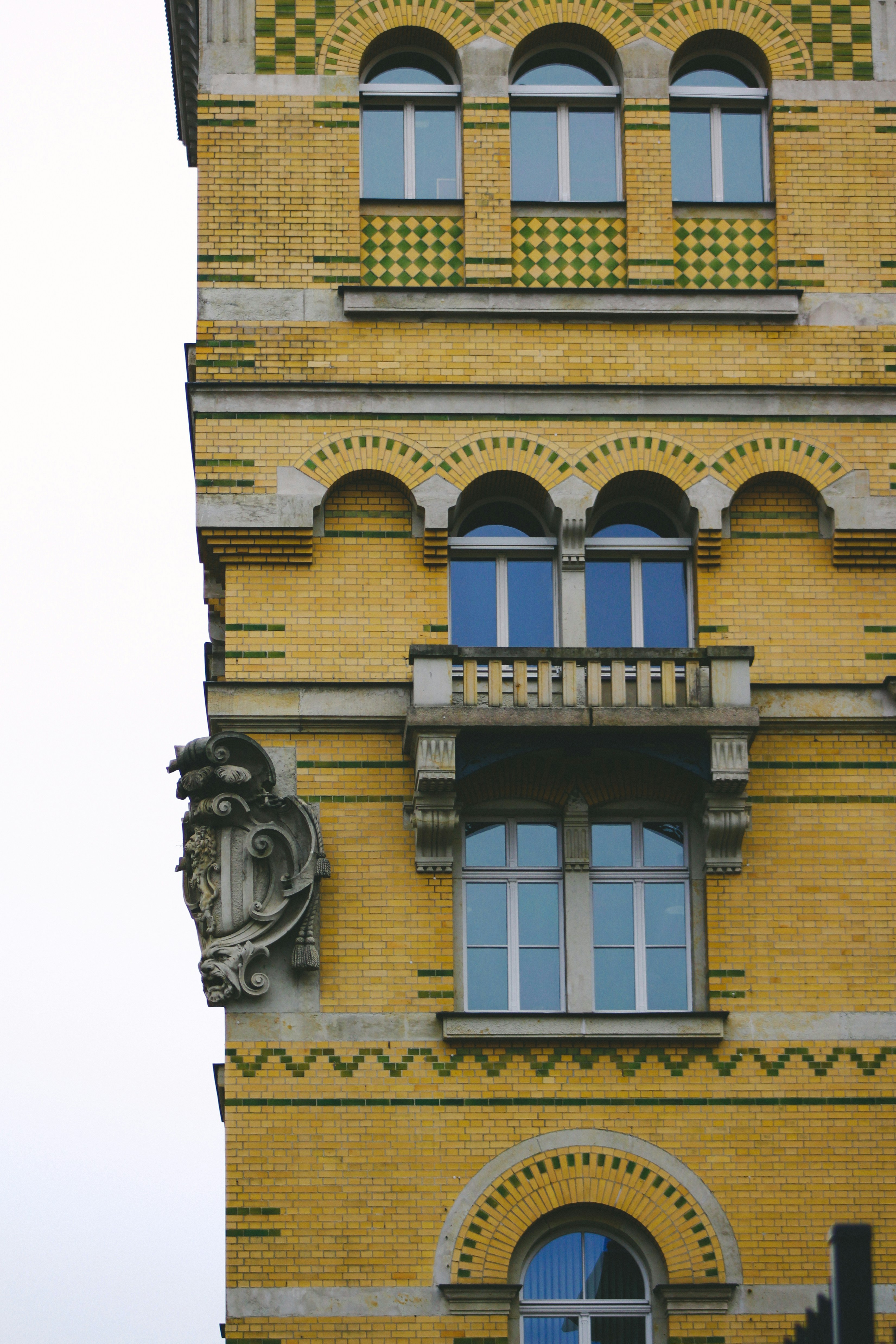 Sunlit Yellow Brick Corner: Arches, Balcony, and a Carved Stone Relief