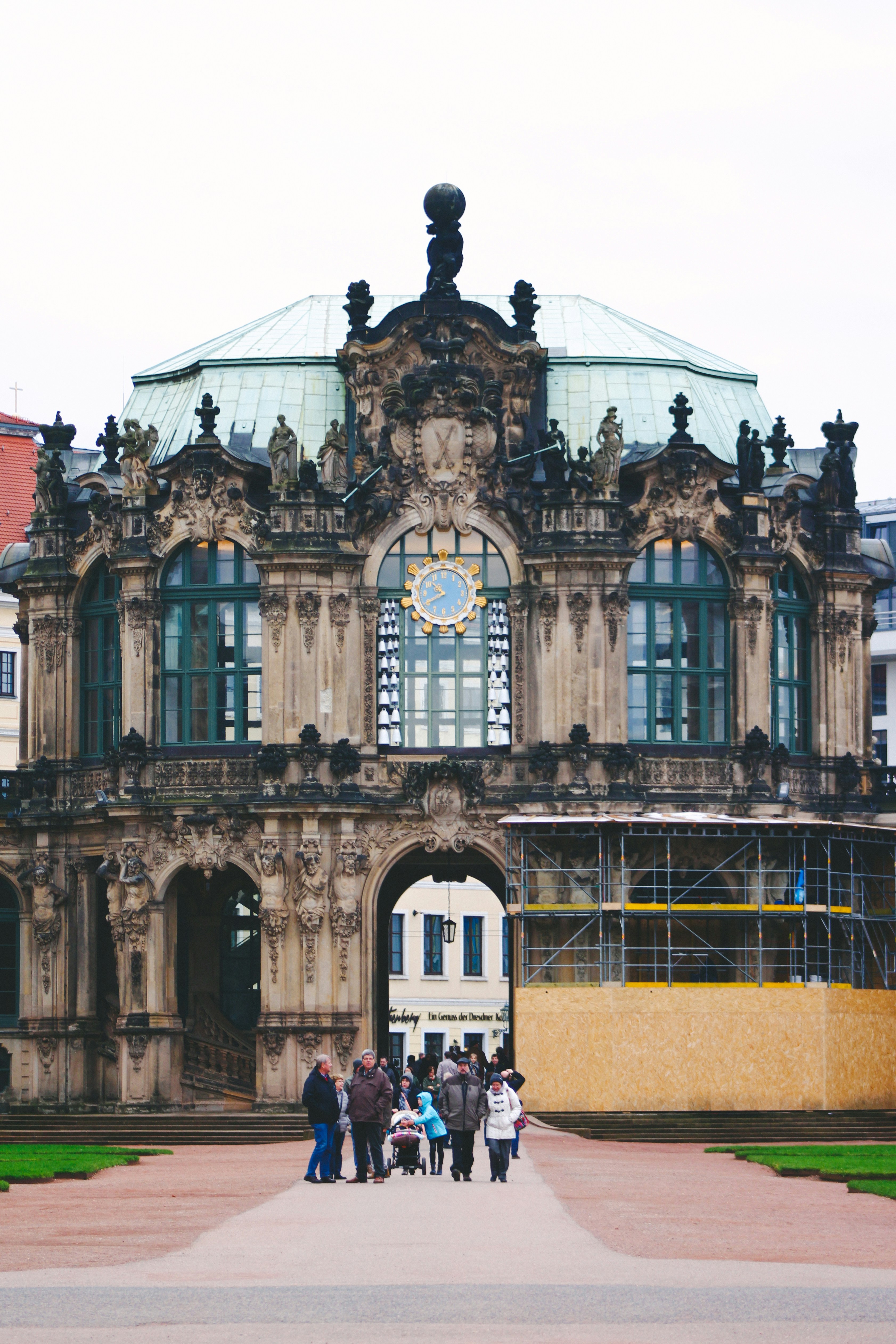 Ornately designed historic pavilion in Dresden with visitors walking towards the entrance. The structure showcases intricate details and a vibrant clock.