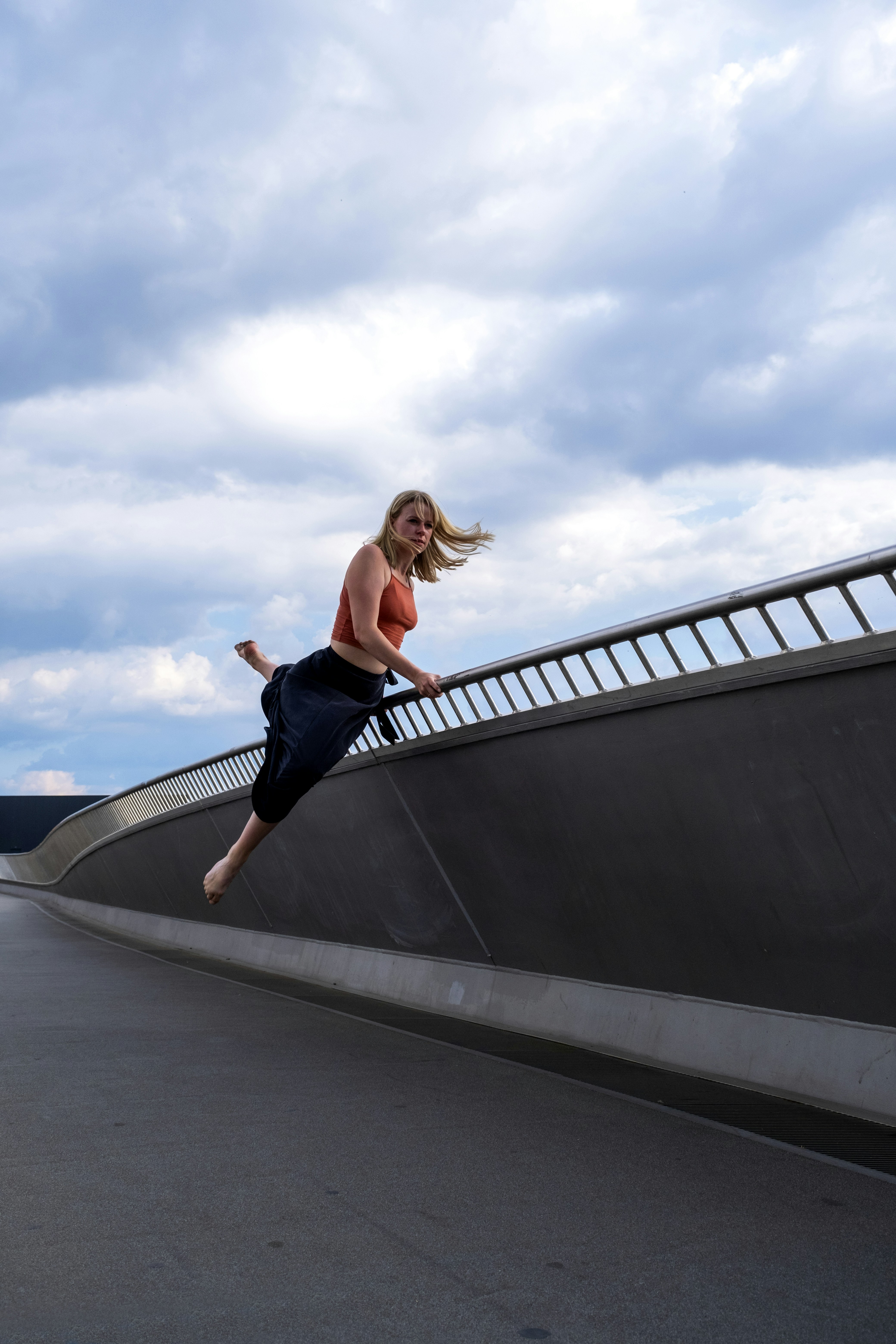 A woman leaps gracefully over a modern architectural structure under a dramatic sky, showcasing a blend of movement and design.