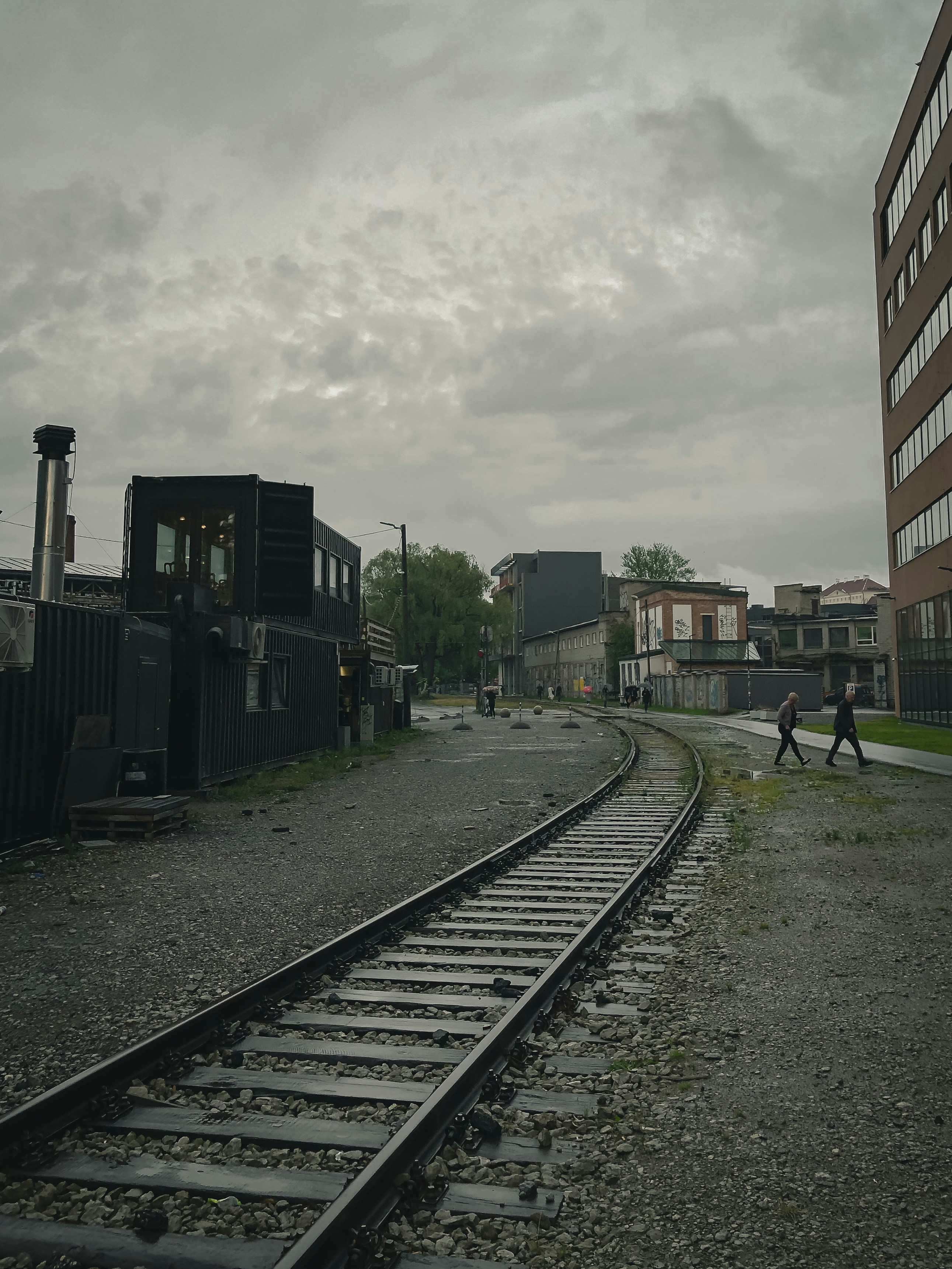 Curved railway tracks meander past industrial buildings under a cloudy sky, hinting at a forgotten era of transportation.