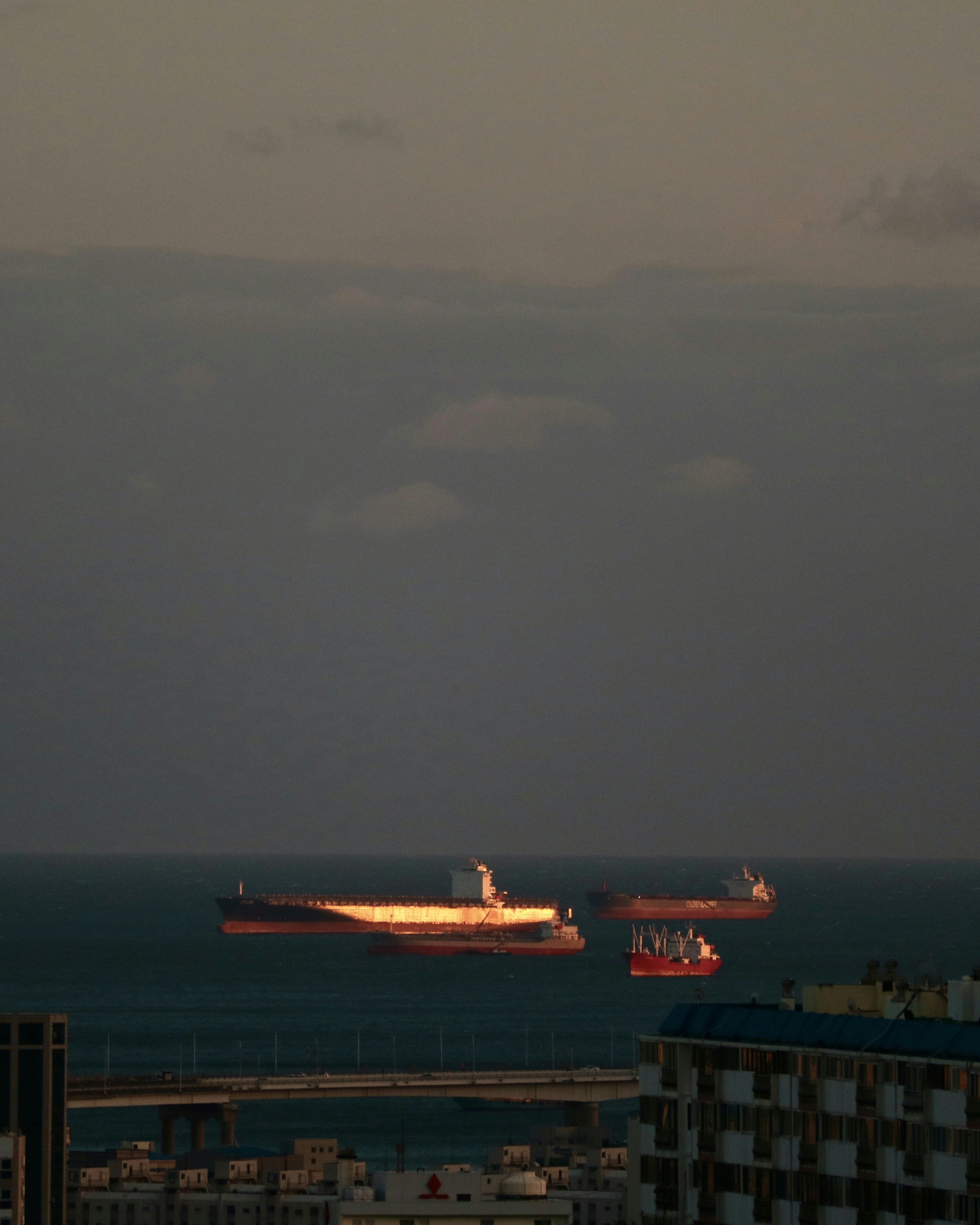 Cargo ships anchored in a tranquil harbor under a twilight sky, reflecting soft hues of sunset on the water's surface.