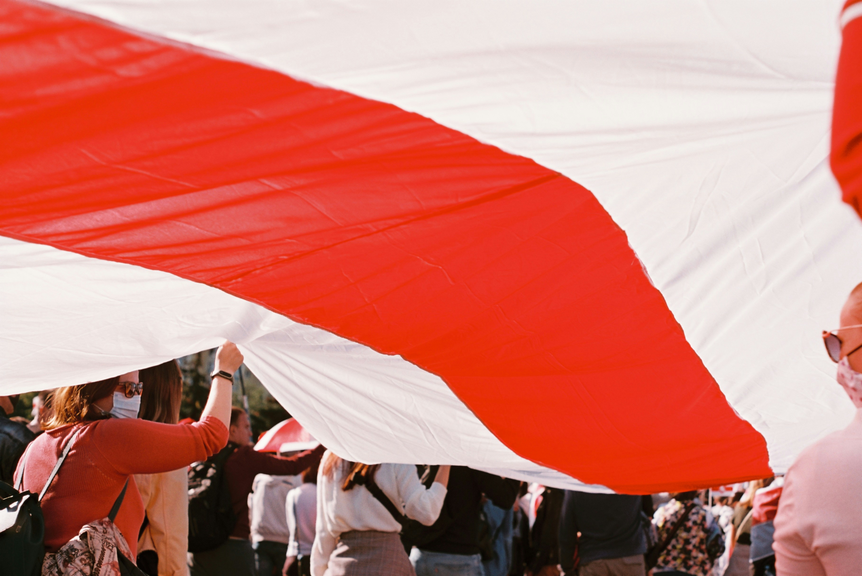 People holding a large red and white flag during a public gathering.