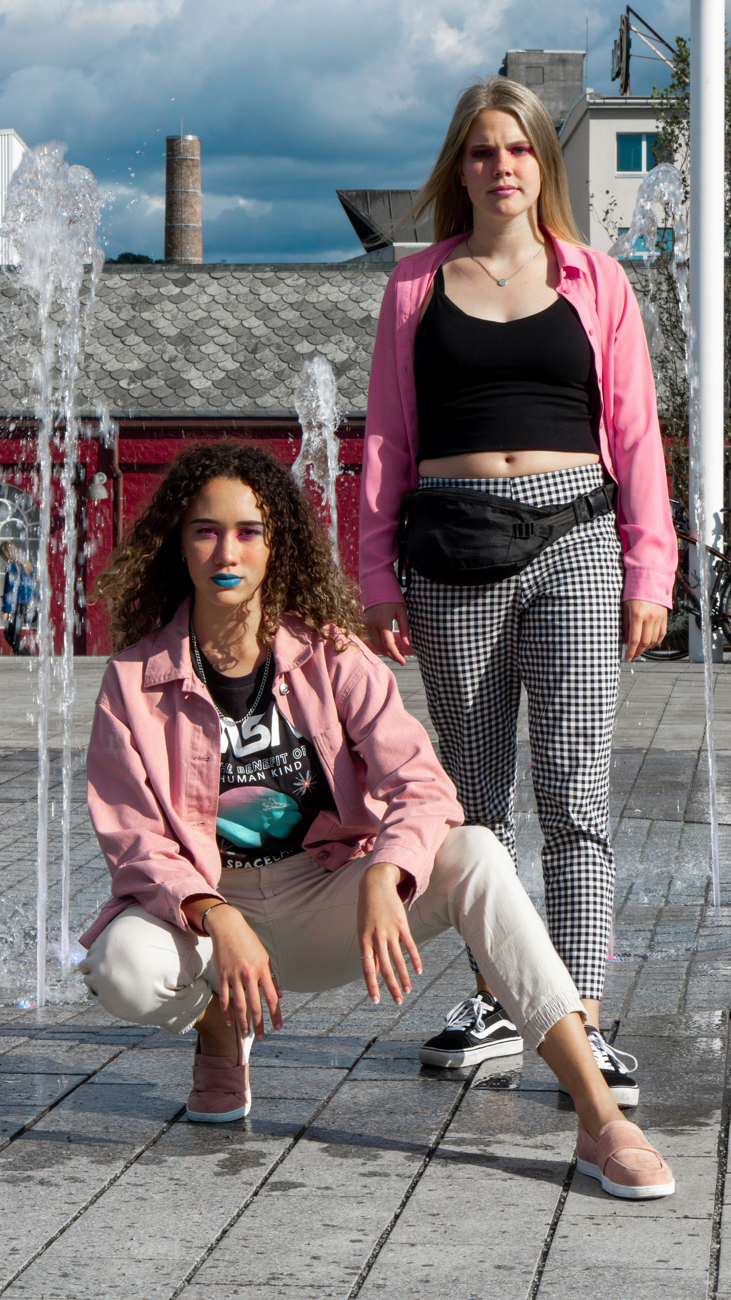 Urban Reflections: Pink-Jacket Duo Framing a City Fountain