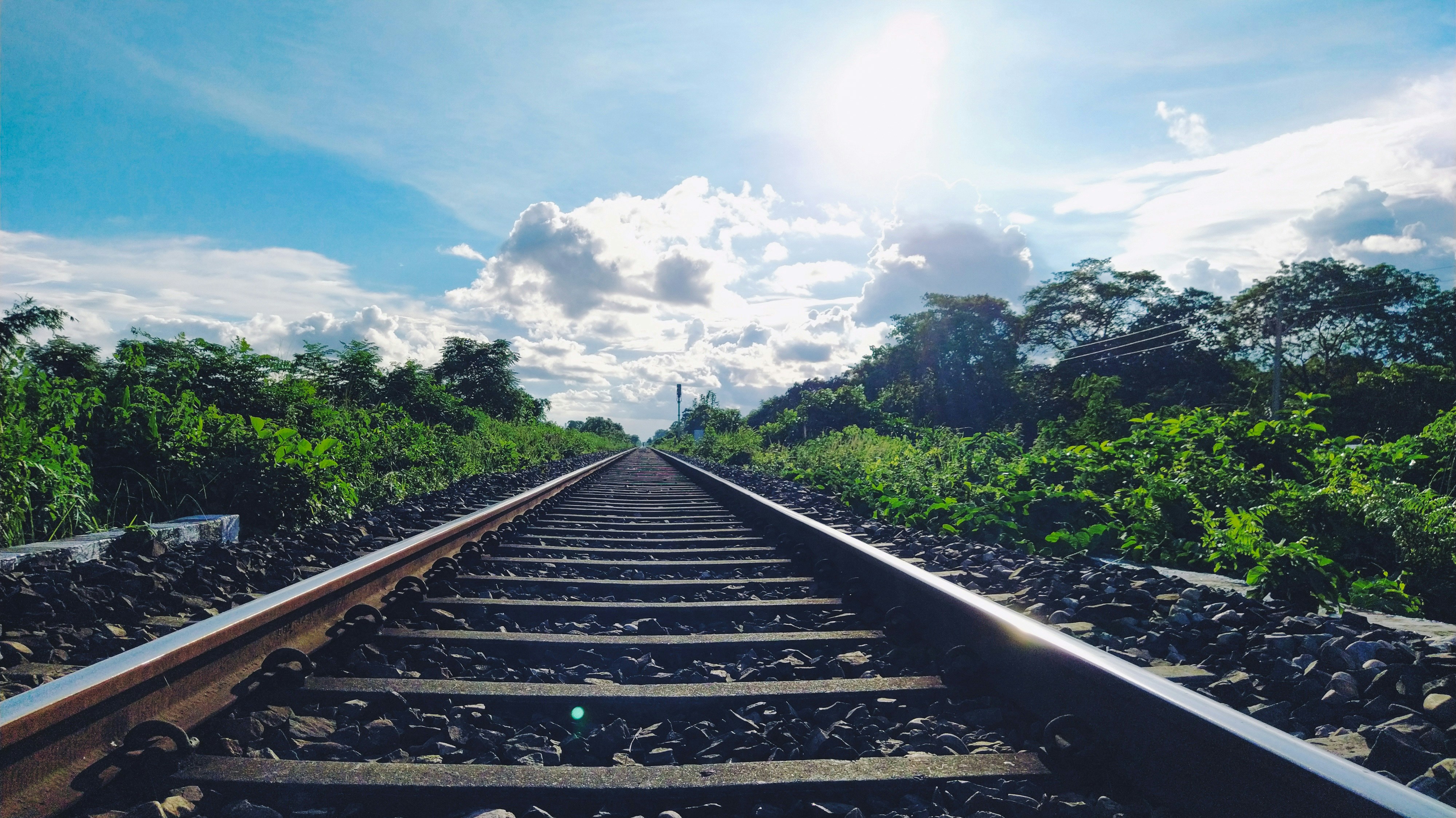 Railway tracks stretching into the distance beneath a bright blue sky with scattered clouds.