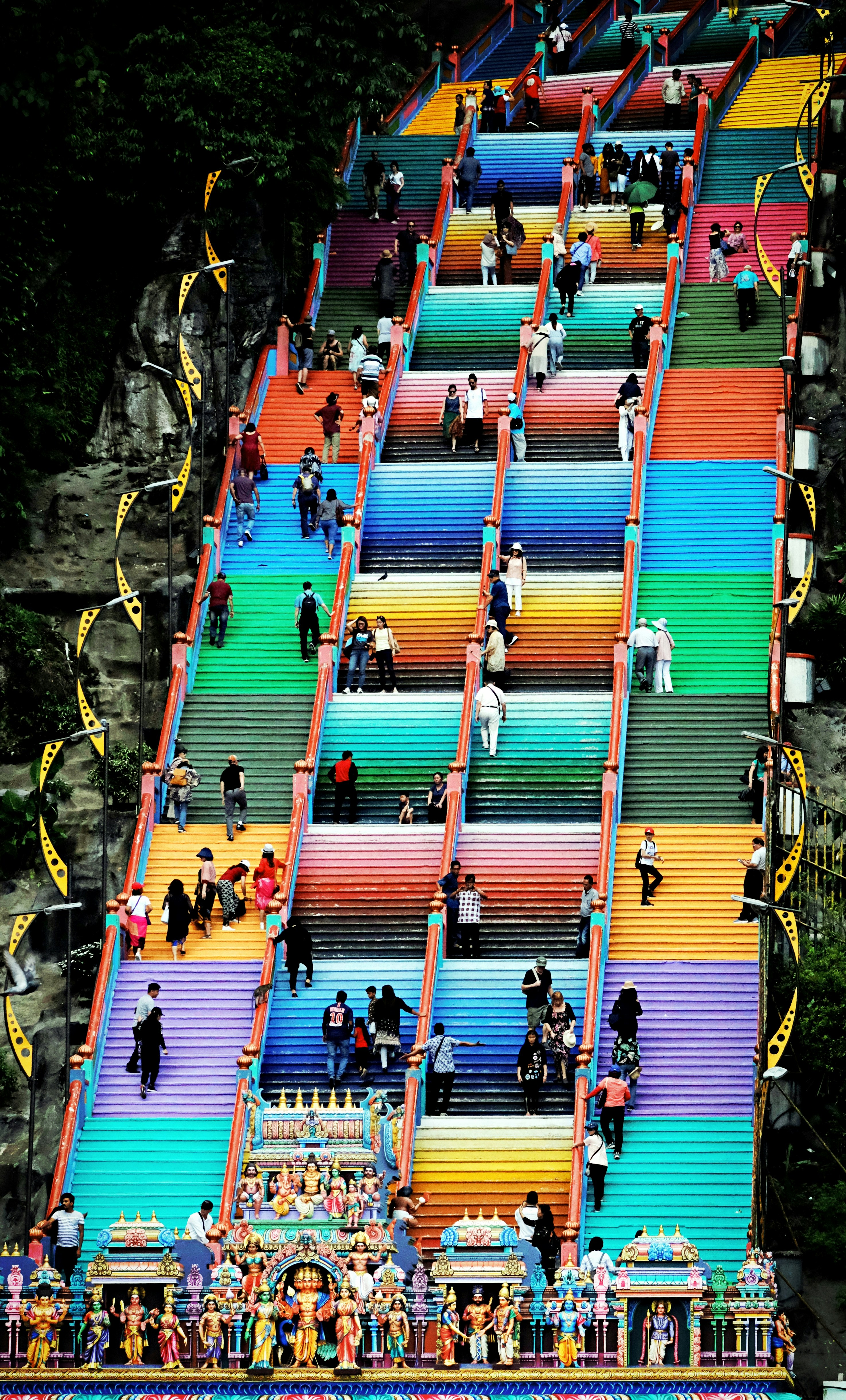 A vibrant staircase at Batu Caves, adorned with a spectrum of colors, leading visitors toward the temple above. The lively scene captures the essence of cultural pilgrimage.