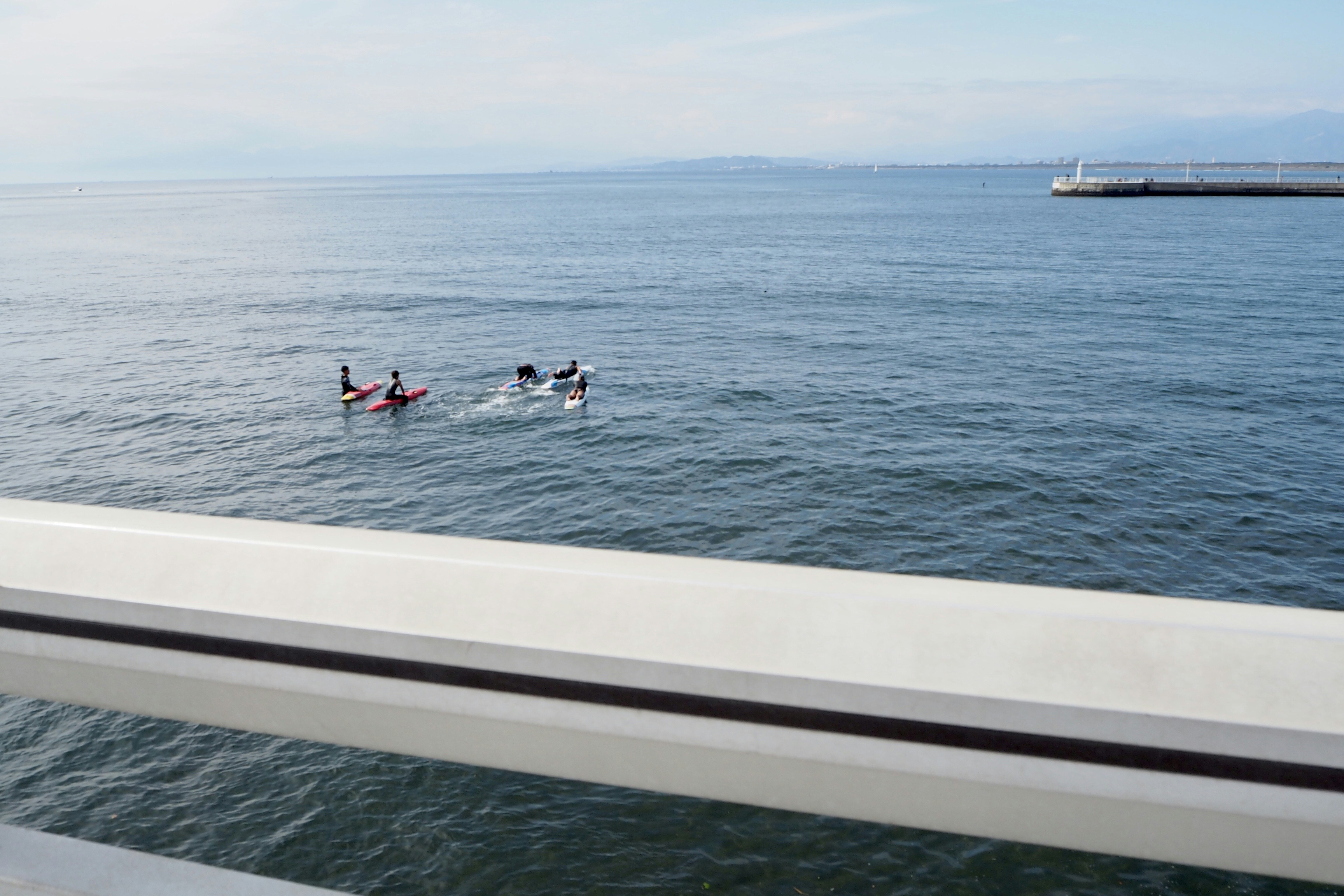 Group of paddleboarders navigating calm waters under a clear sky, framed by a modern structure in the foreground.