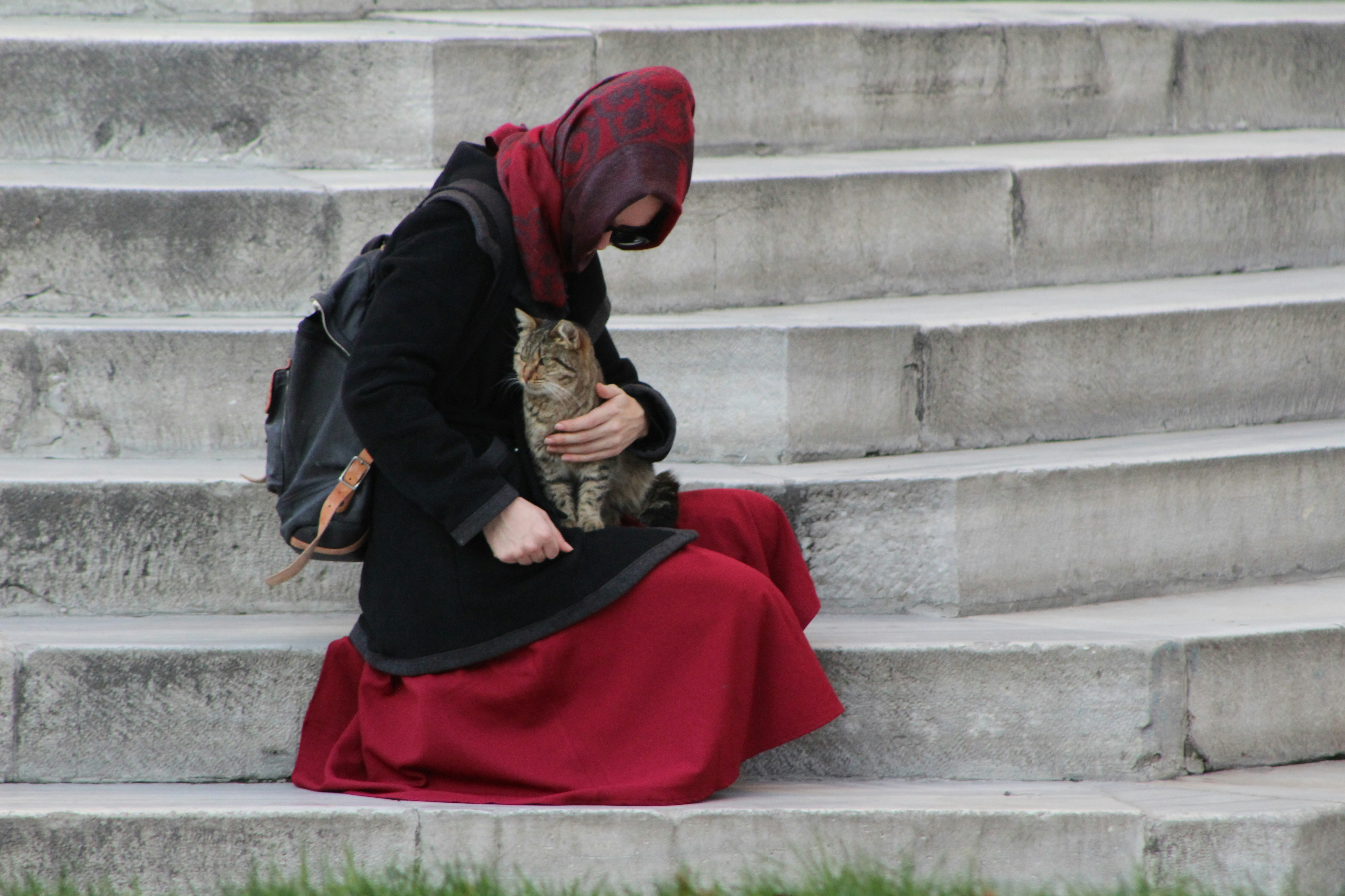 Woman in a red dress holding a cat while seated on stone steps, showcasing a tender moment of companionship.