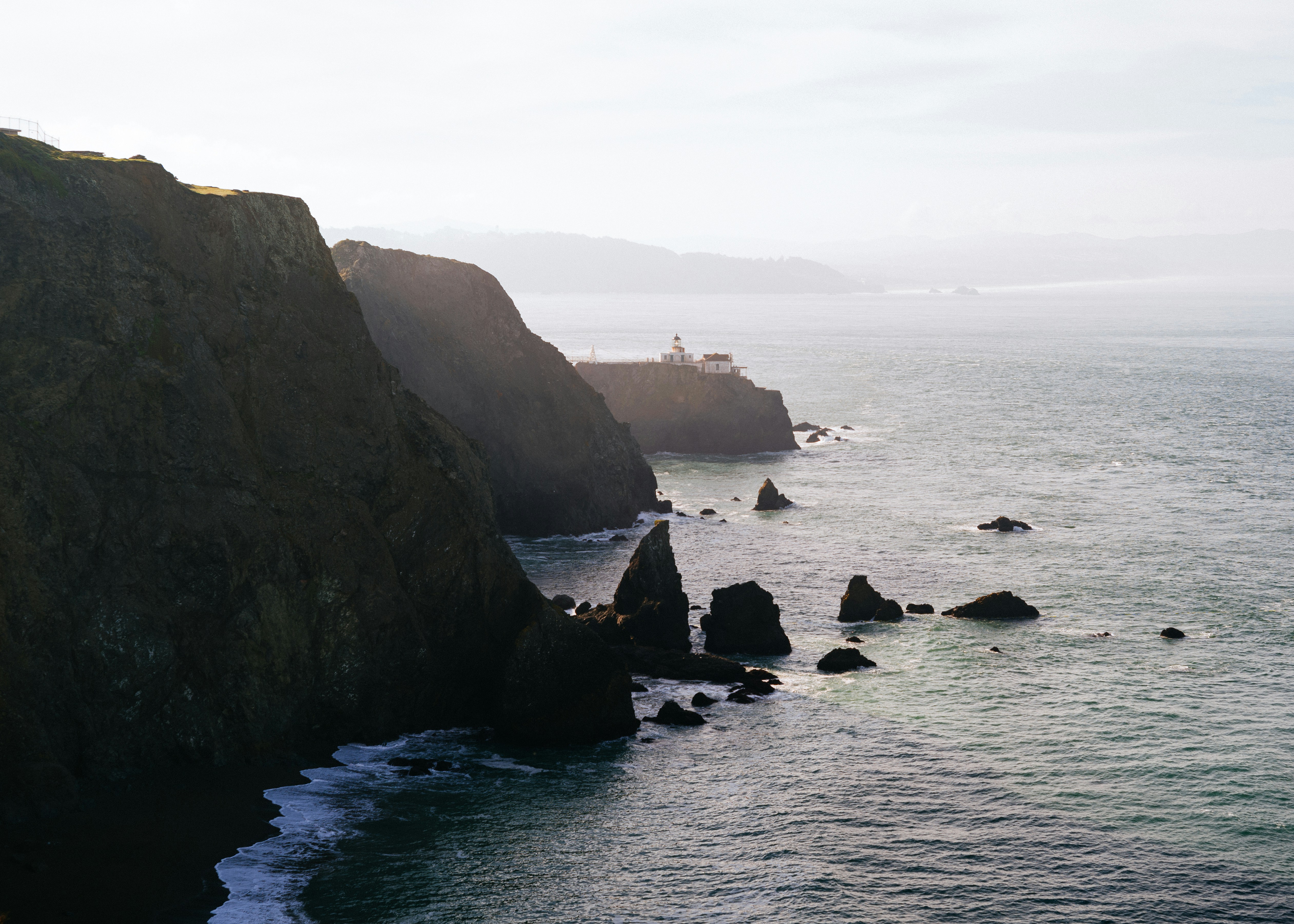A rugged coastline with dramatic rock formations and a distant lighthouse overlooking the serene ocean waves.