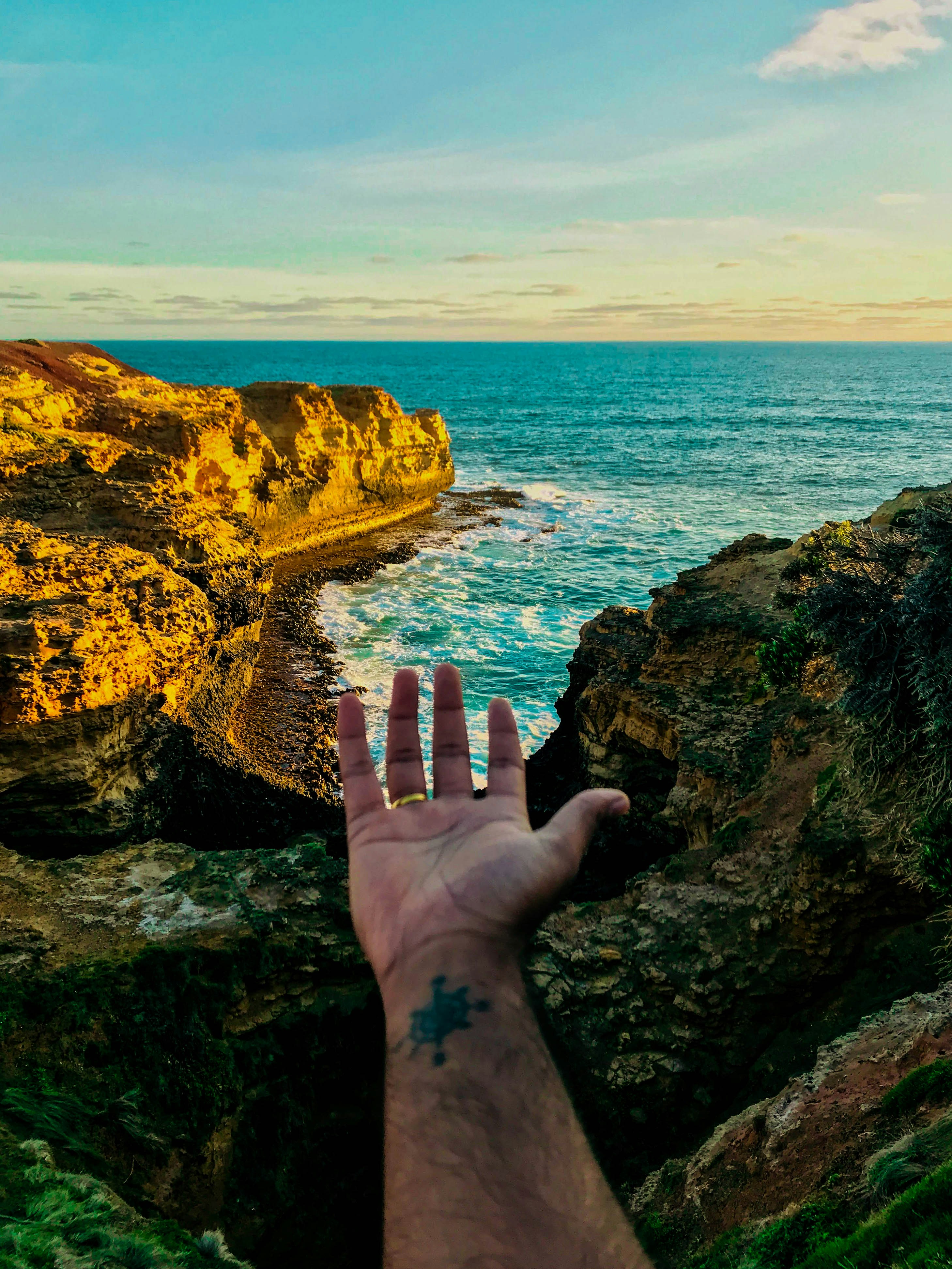 Hand at the Edge: Sunlit Cliffs and Turquoise Sea
