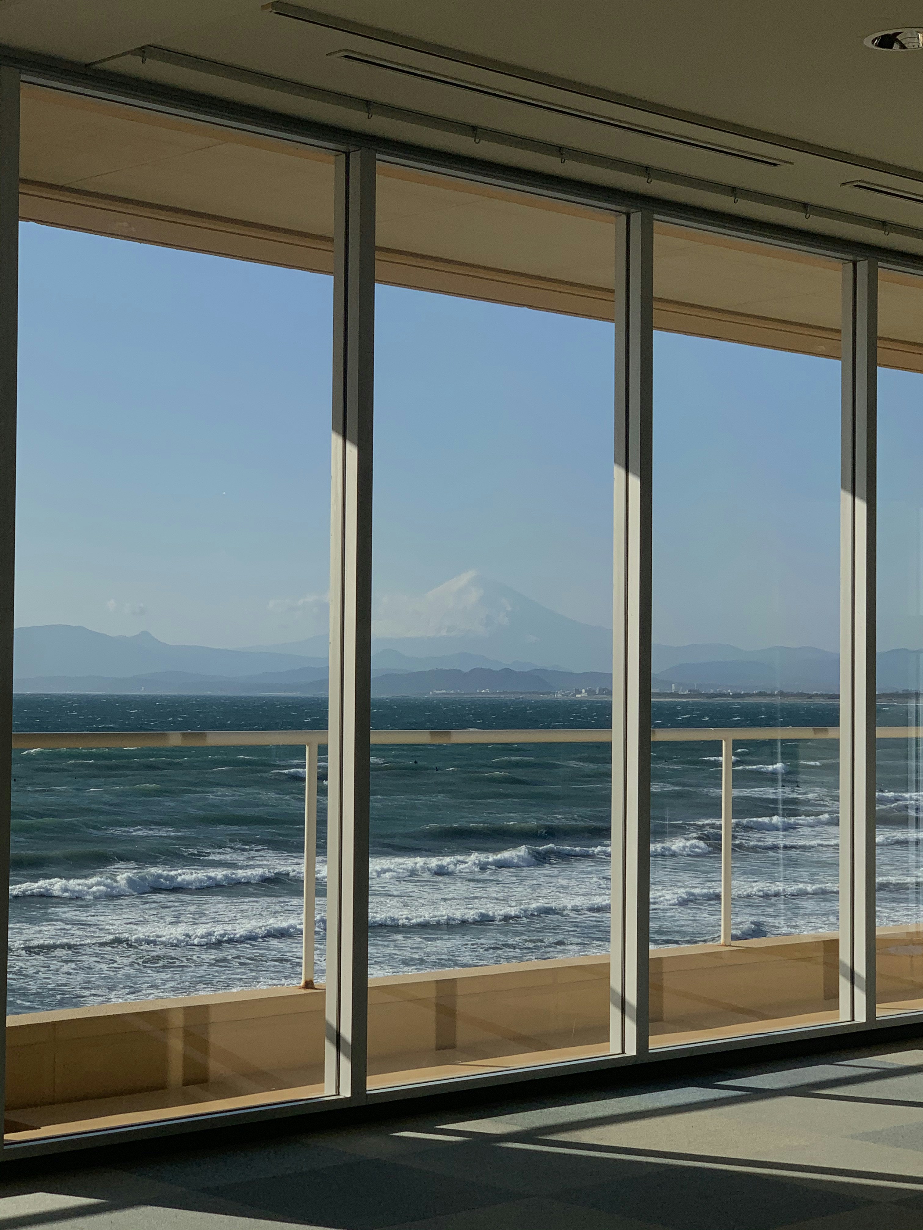 A panoramic view of a serene coastline through large glass windows, with distant mountains creating a tranquil backdrop.