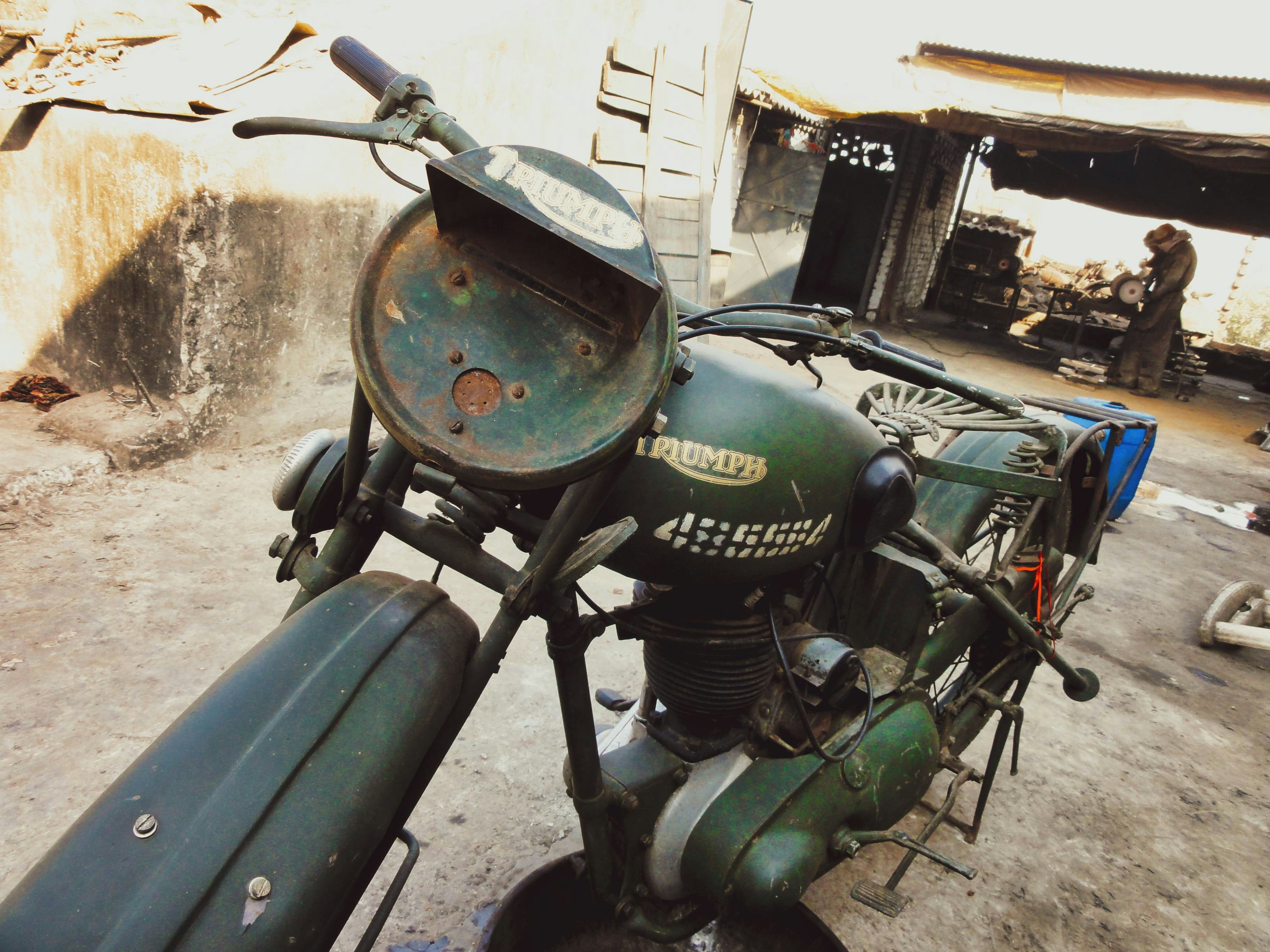 Old green motorcycle with faded paint in a rustic outdoor setting.