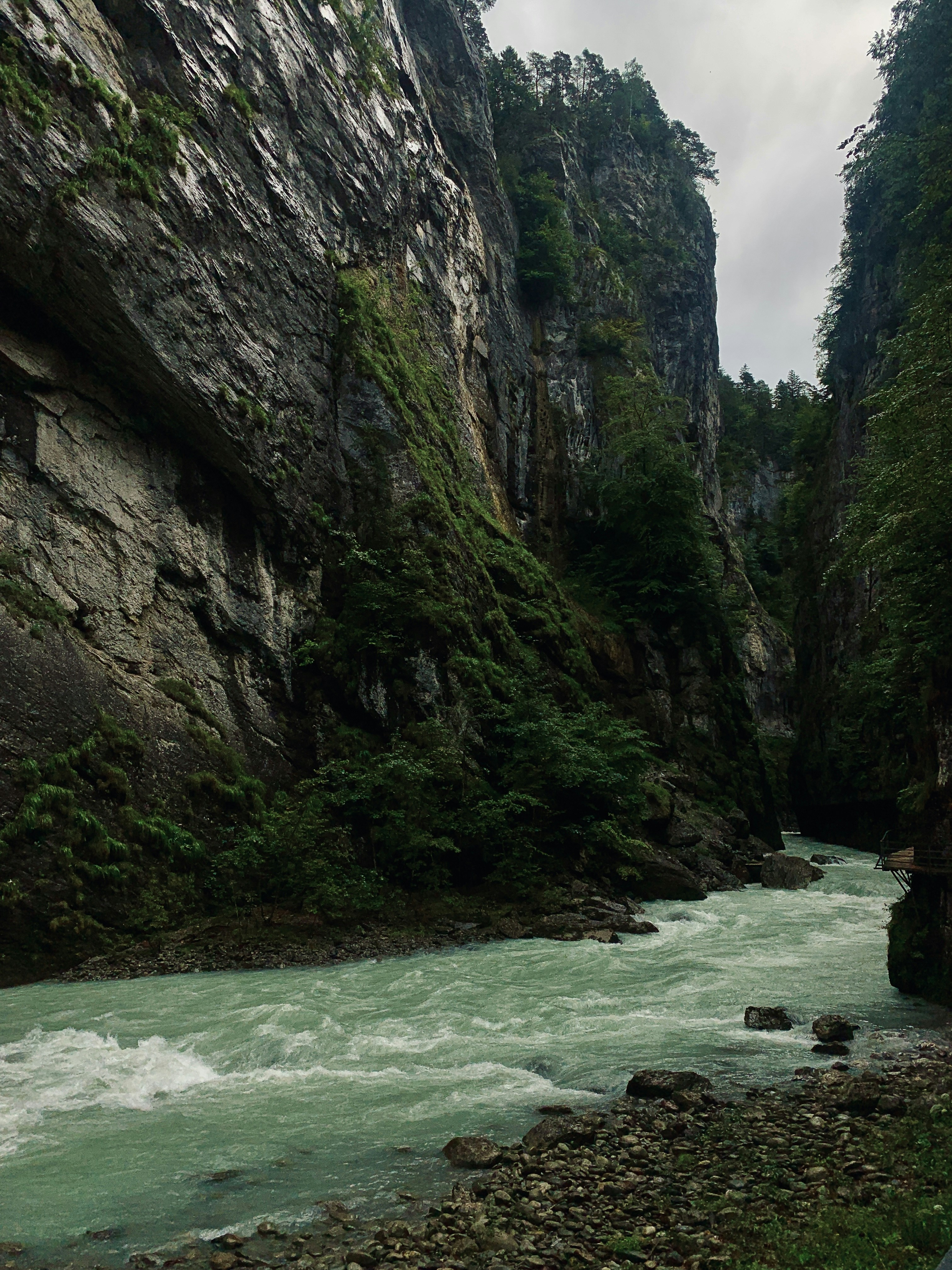 Turquoise river flowing through a narrow canyon surrounded by towering cliffs and lush greenery.
