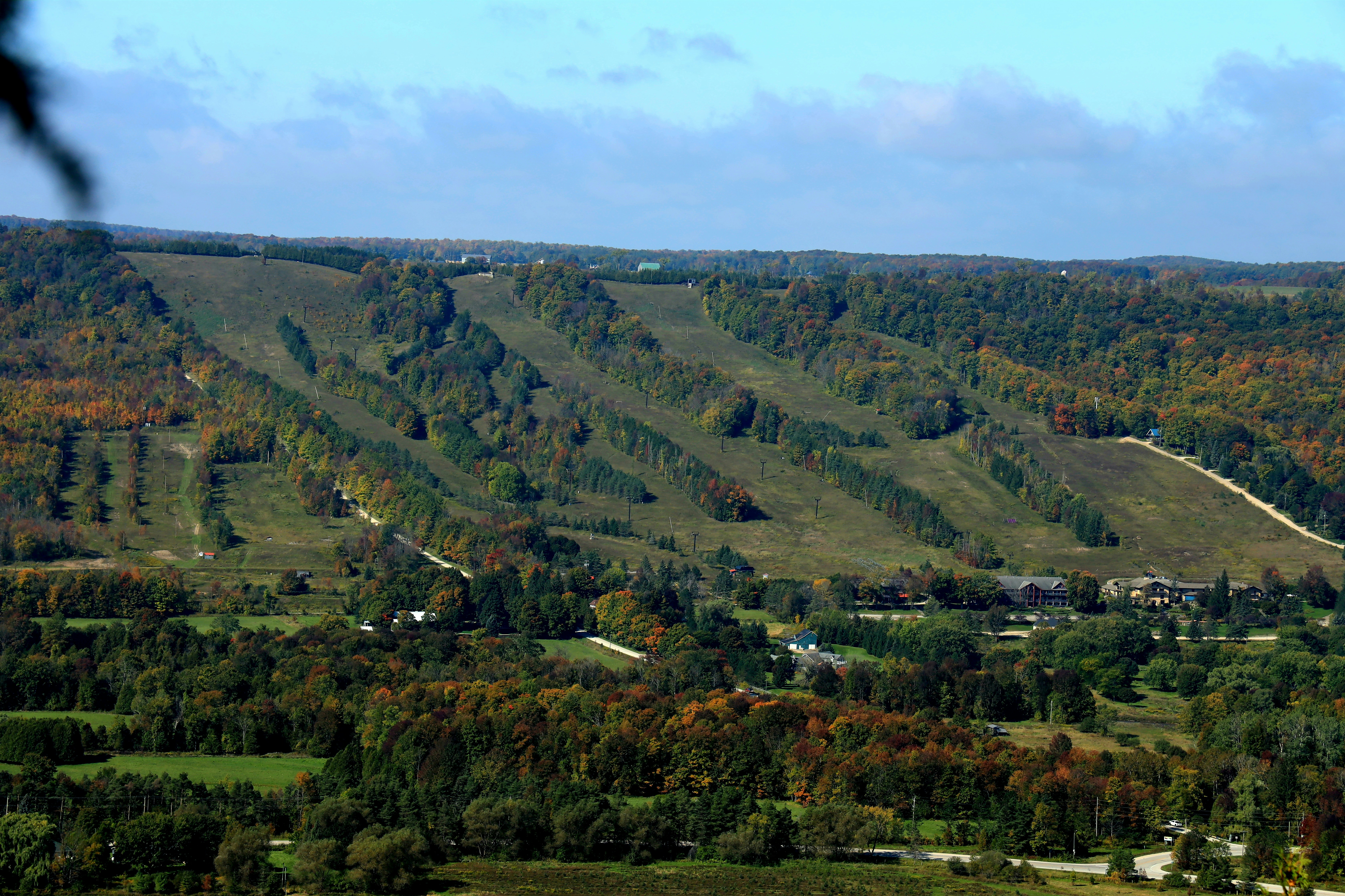 Expansive view of rolling hills showcasing vibrant autumn foliage and ski slopes, with a serene valley below.