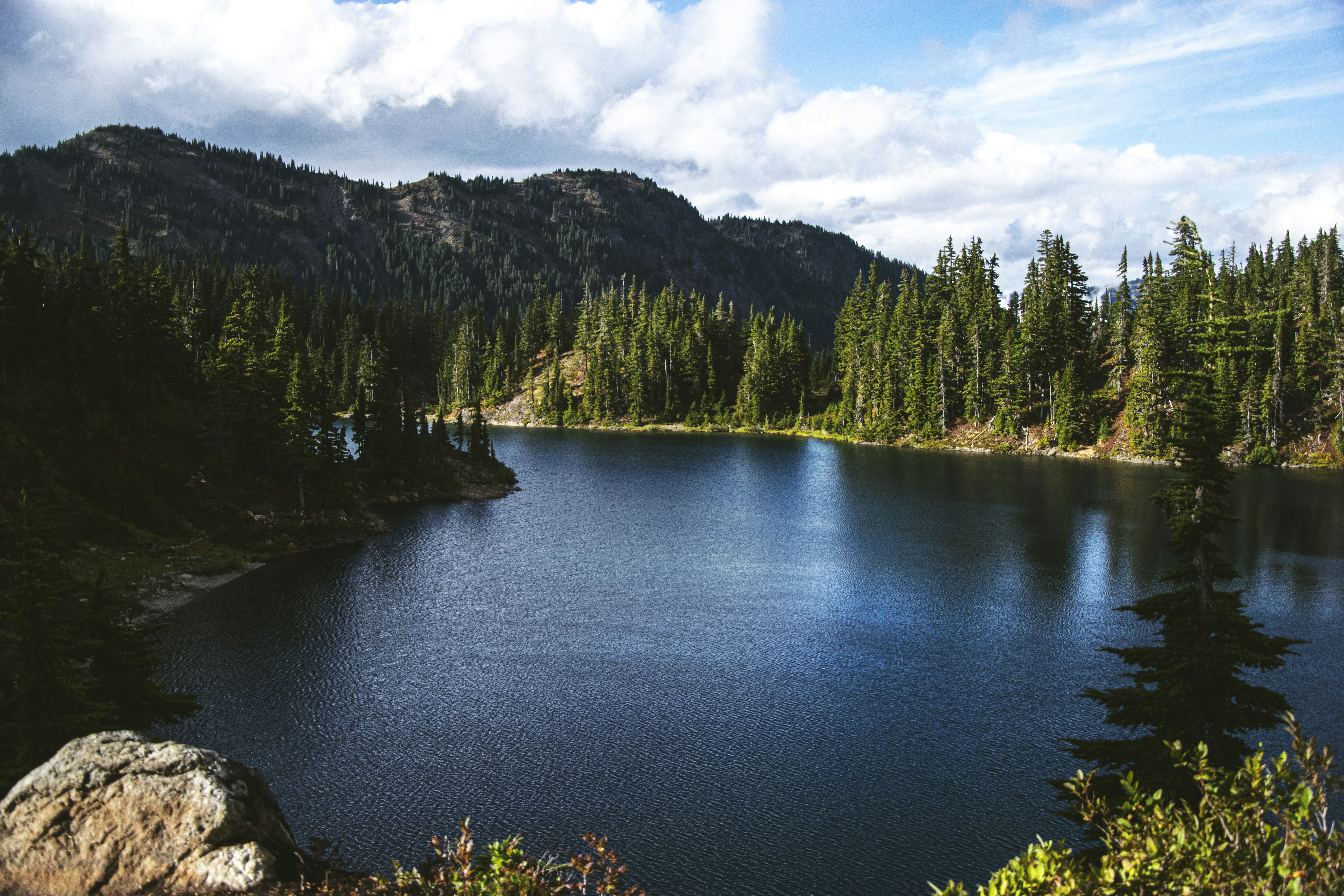 Serene mountain lake surrounded by dense evergreens under a cloudy sky.