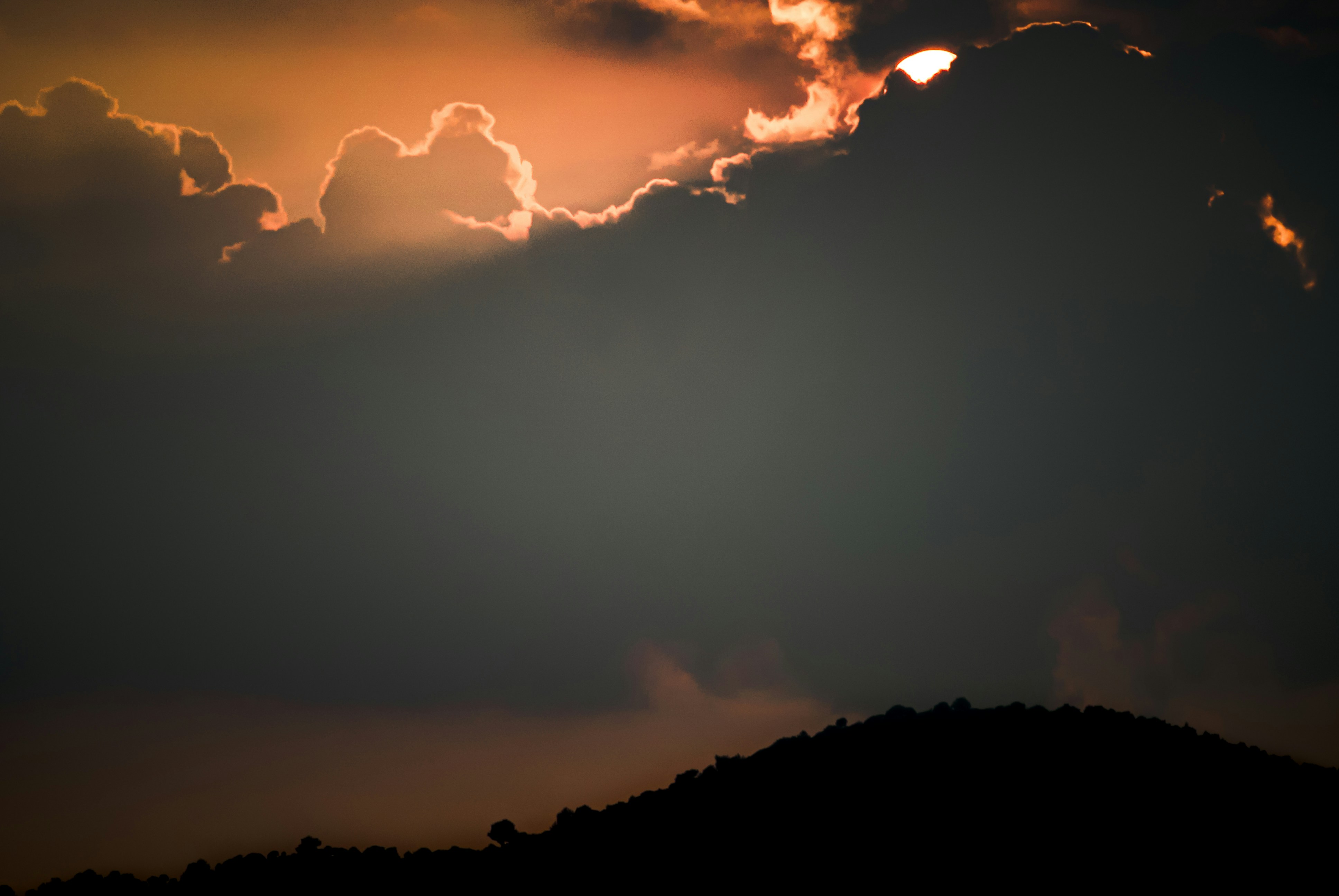 Dark clouds illuminated by a fading sunset, casting an ethereal glow over a distant silhouette of hills.