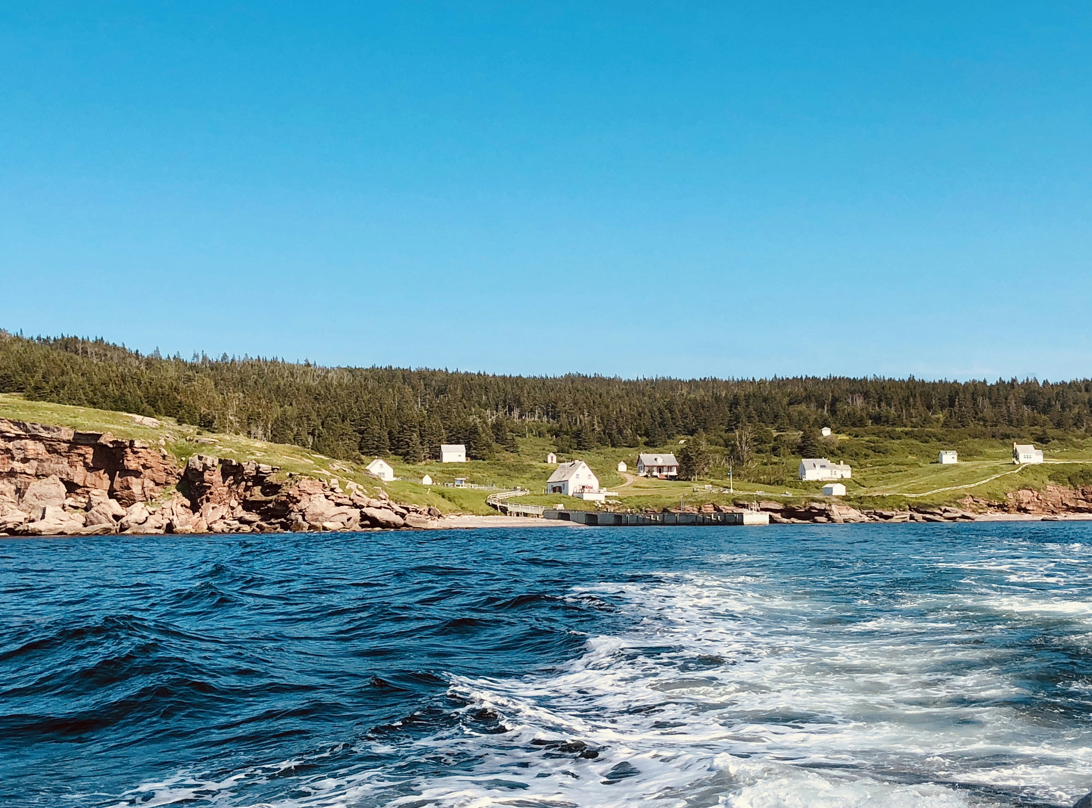 White cabins scattered along a green hillside by the ocean under a clear blue sky.