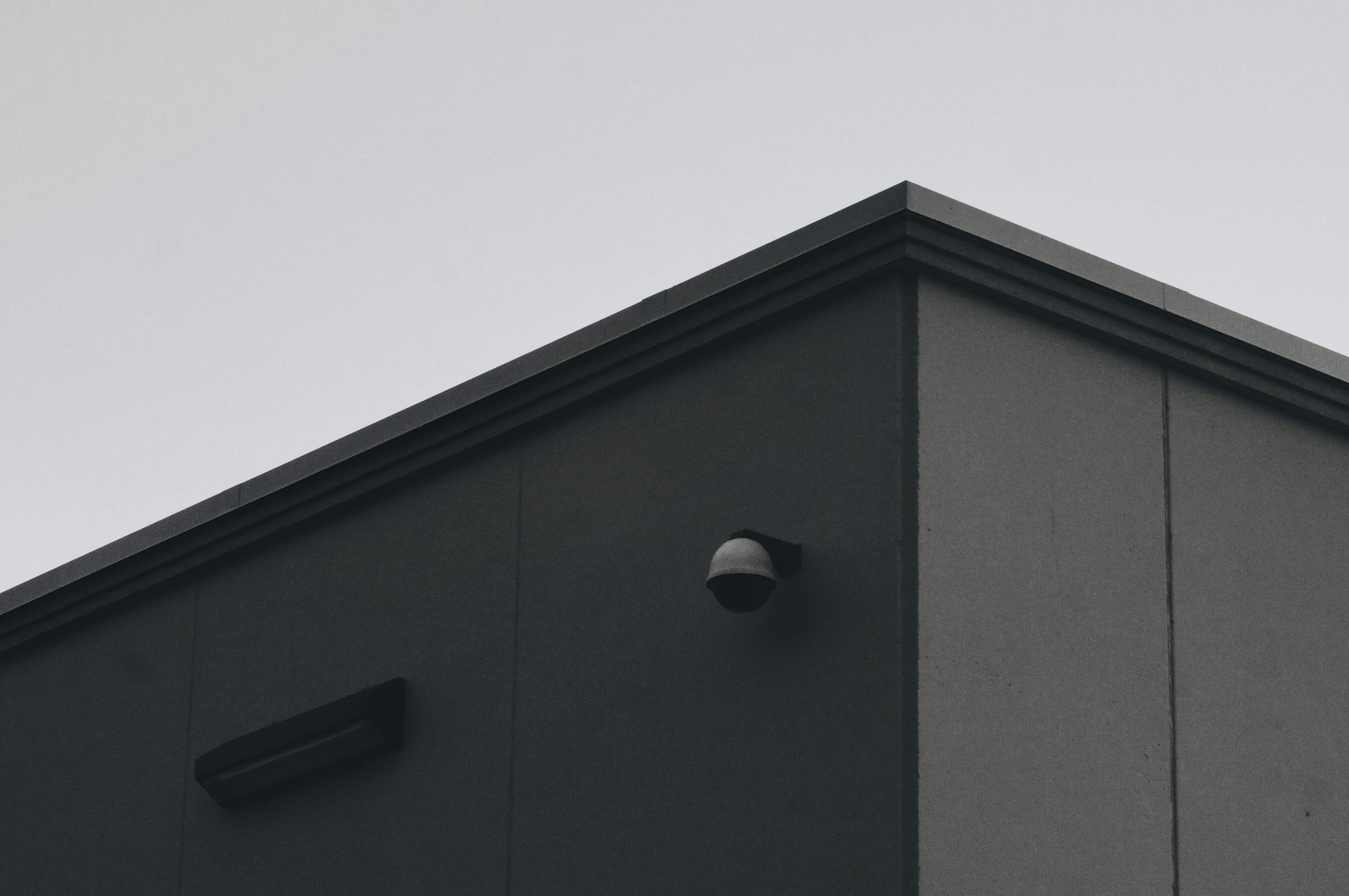 Security camera mounted on a stark corner of a building under an overcast sky.