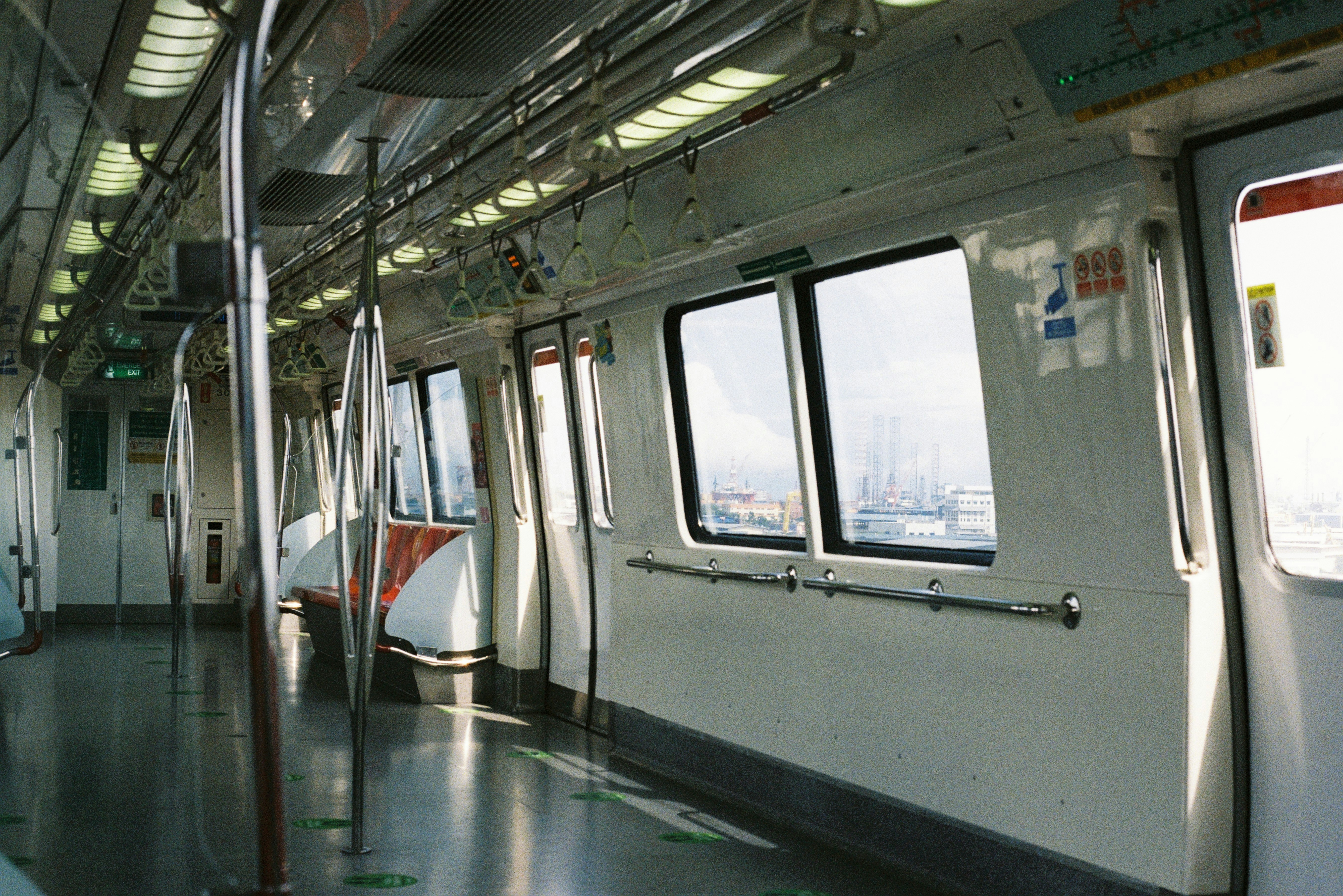 An empty subway car with a long orange bench along the left, metal handrails, and large windows revealing a cityscape outside.