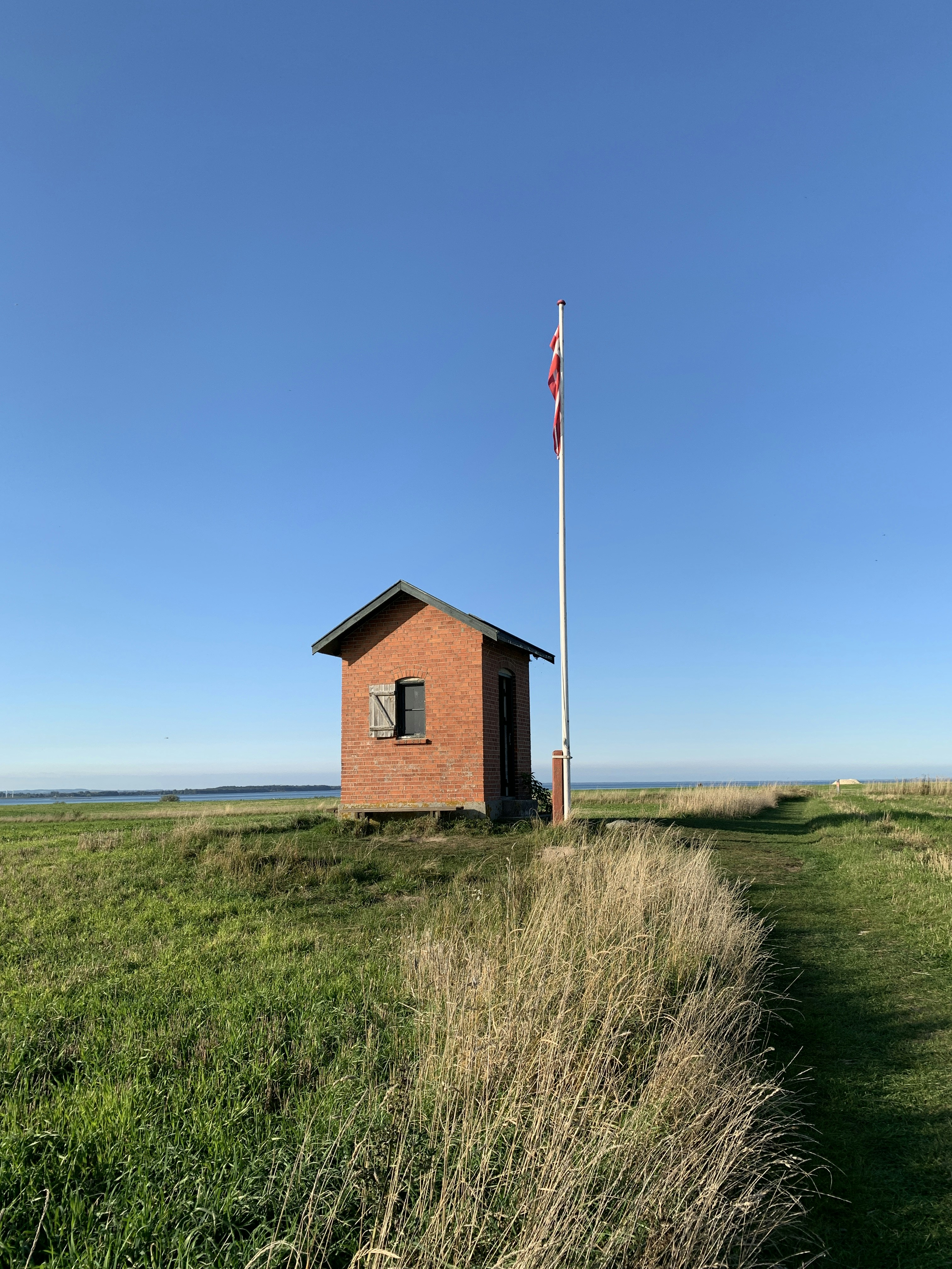 Flagpole Sentinel Beside a Brick Structure on Open Coastal Grassland