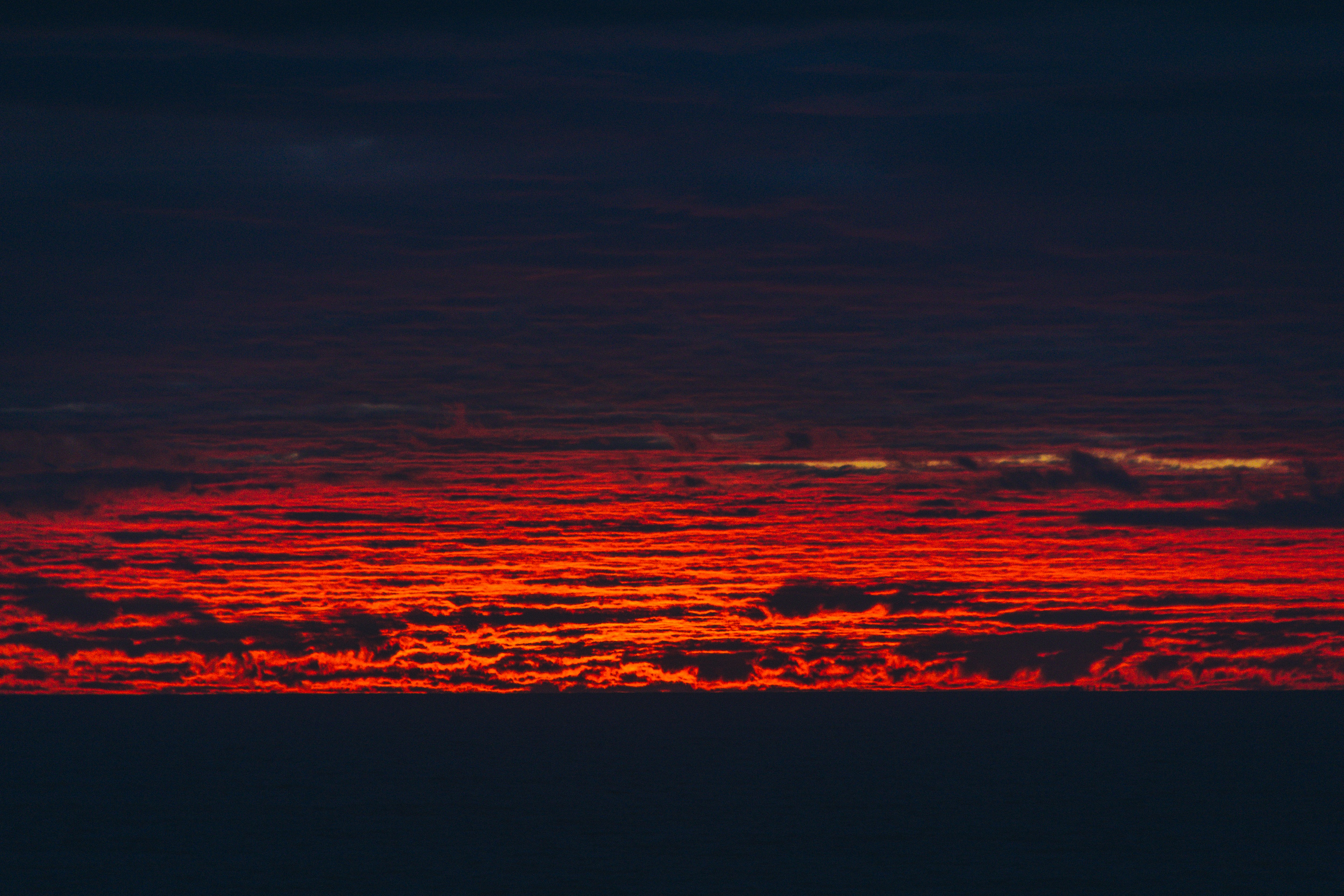 Vibrant sunset casting deep red and orange hues across a layered sky, creating a dramatic contrast against the darkening ocean below.
