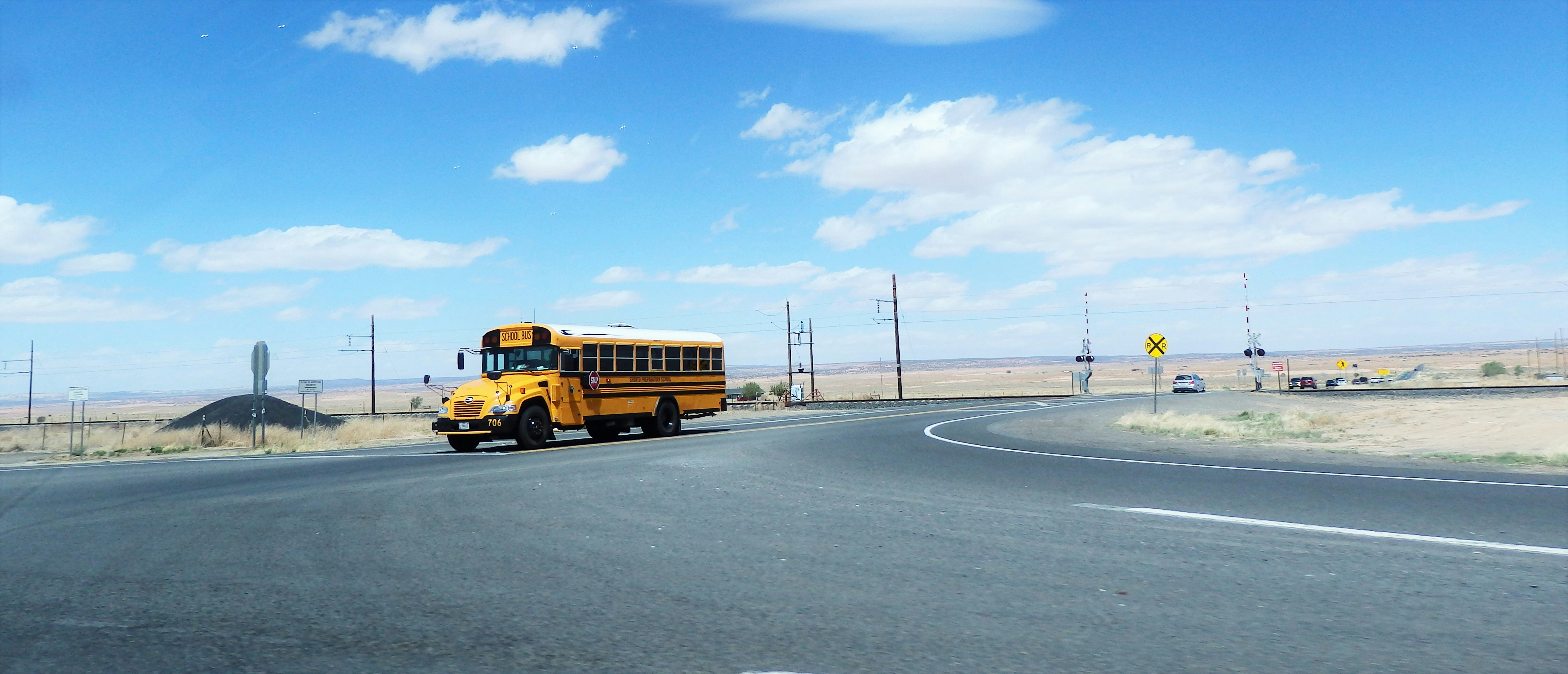 Yellow school bus navigating a winding road under a vast blue sky with scattered clouds.