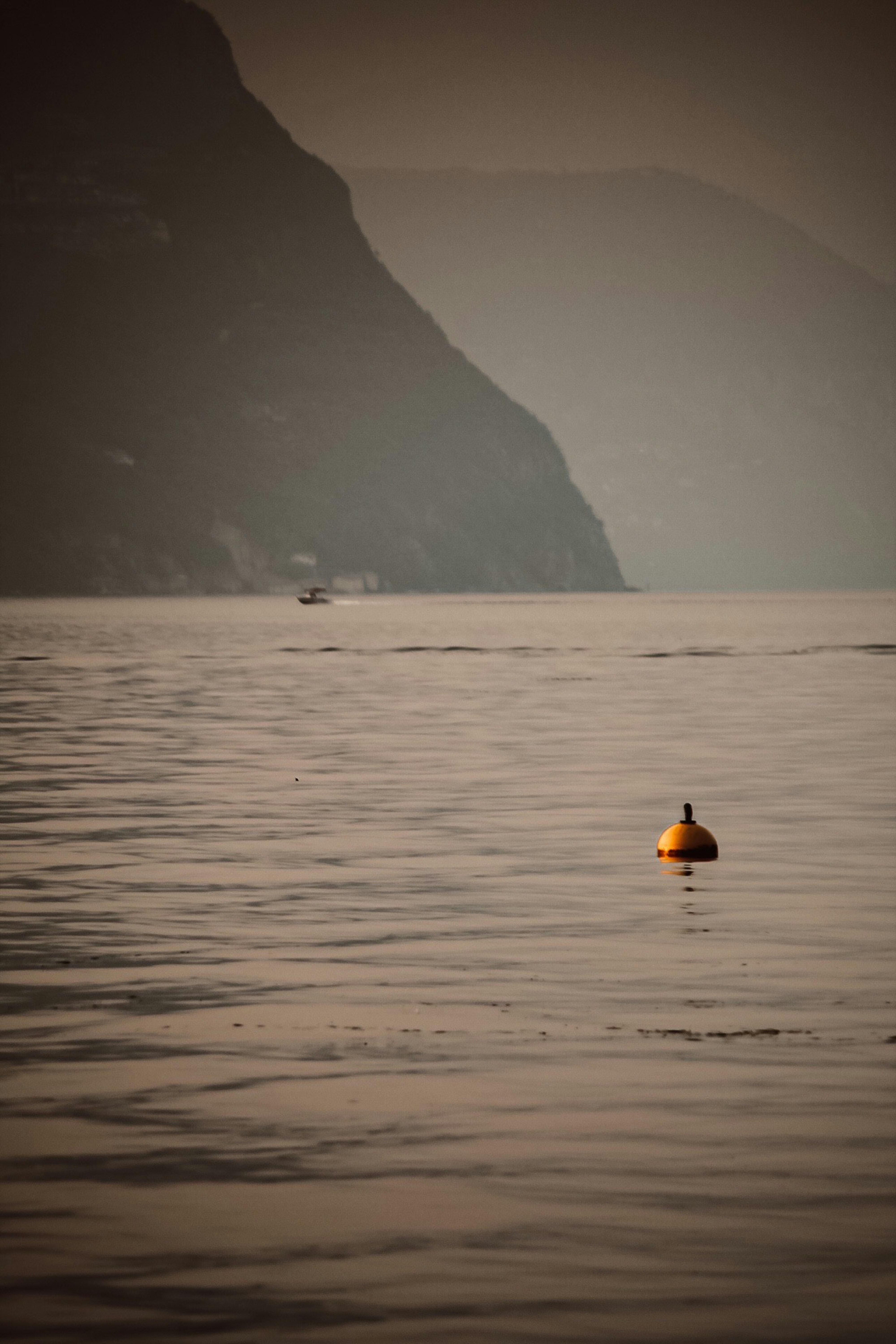 Orange buoy floats on calm water with misty mountains in the background.