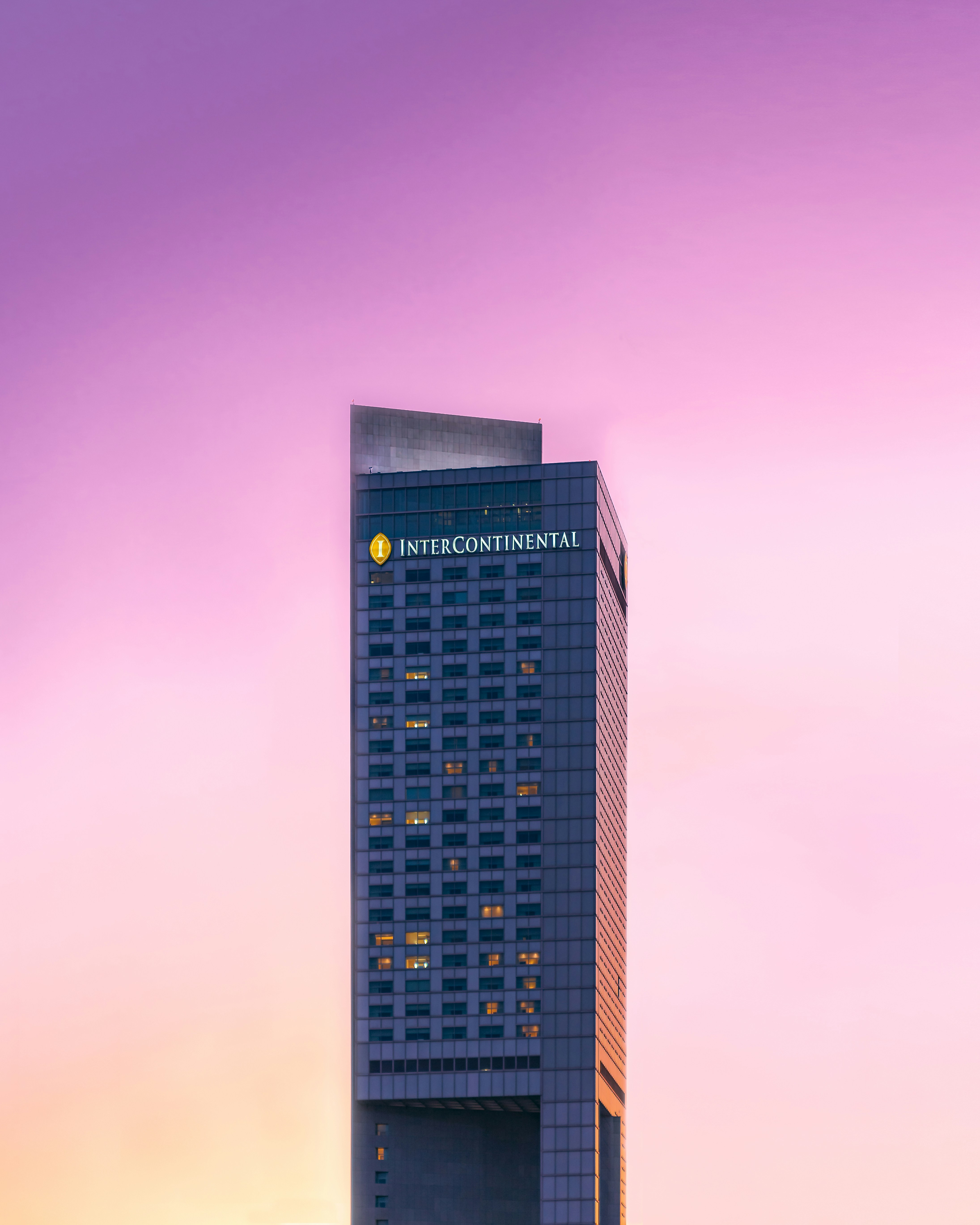 The Intercontinental hotel stands tall against a soft pastel sky, showcasing modern architecture and illuminated windows.