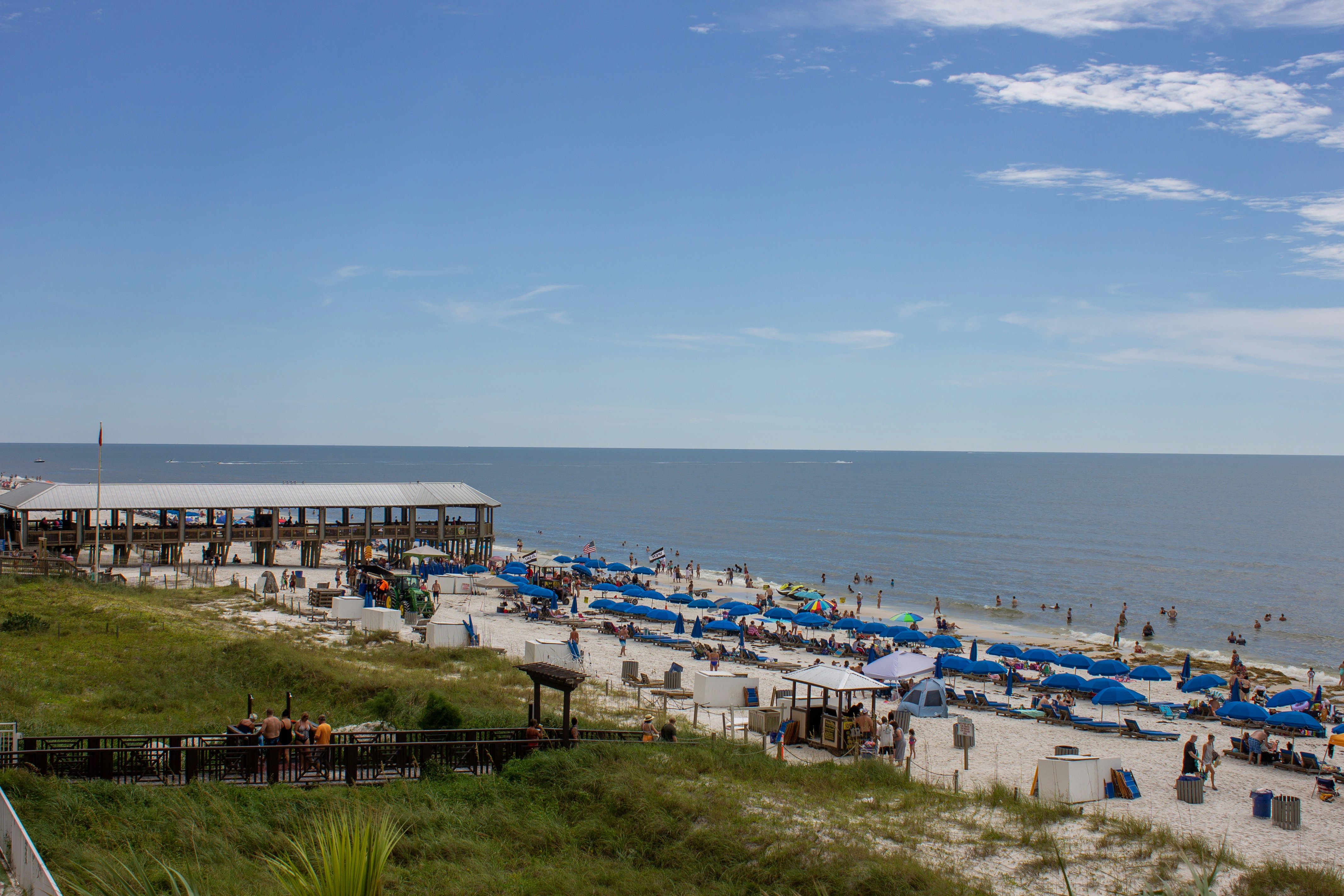 Blue Umbrella Spine and a Weathered Pier Stretching Over a Busy Beach