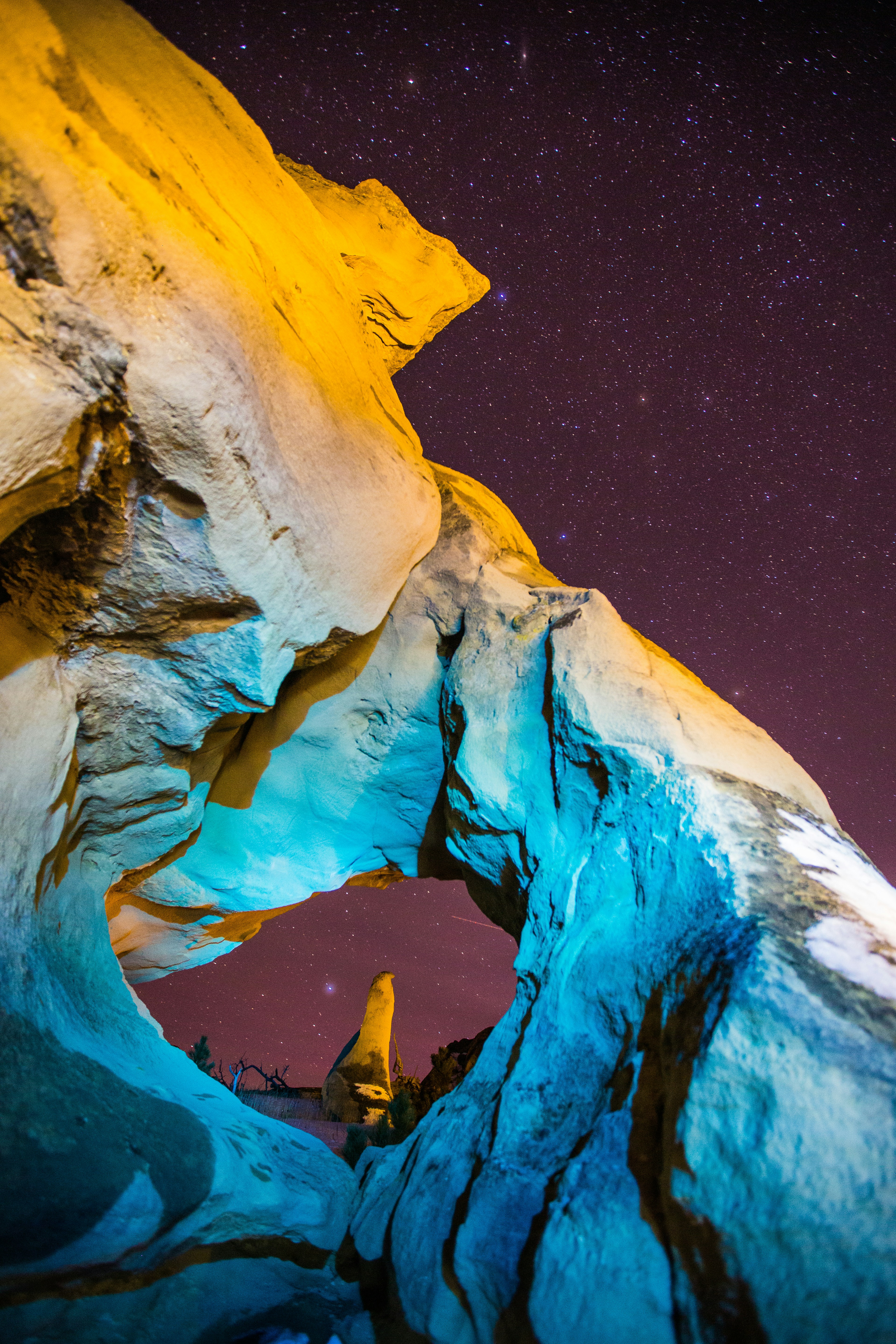 Illuminated rock arch framing a starry sky, showcasing vibrant colors and unique geological formations.
